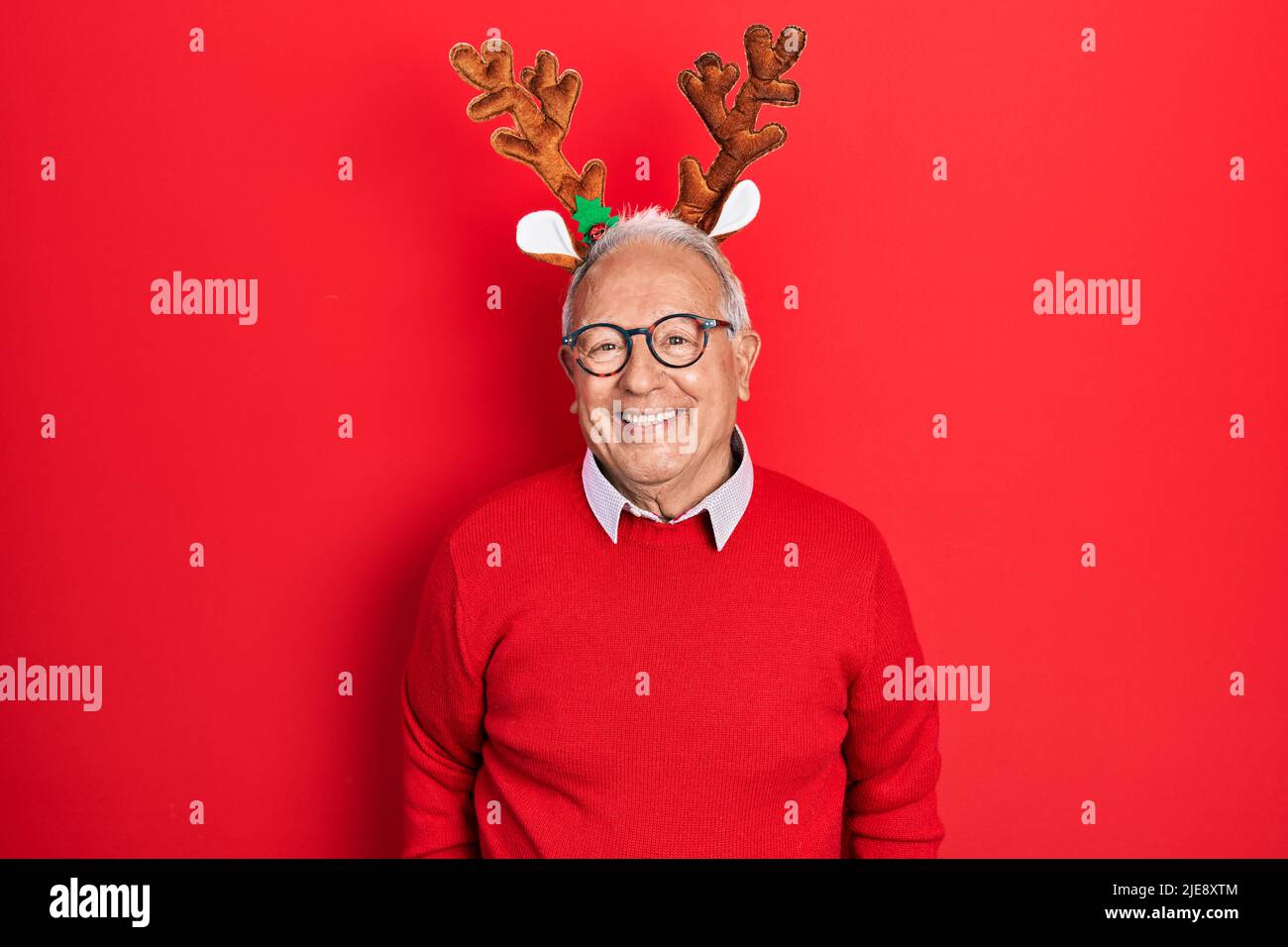 Senior man with grey hair wearing deer christmas hat looking positive ...