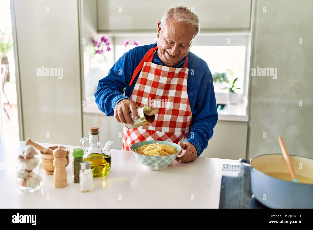 Senior man smiling confident pouring tomato sauce on spaghetti at ...