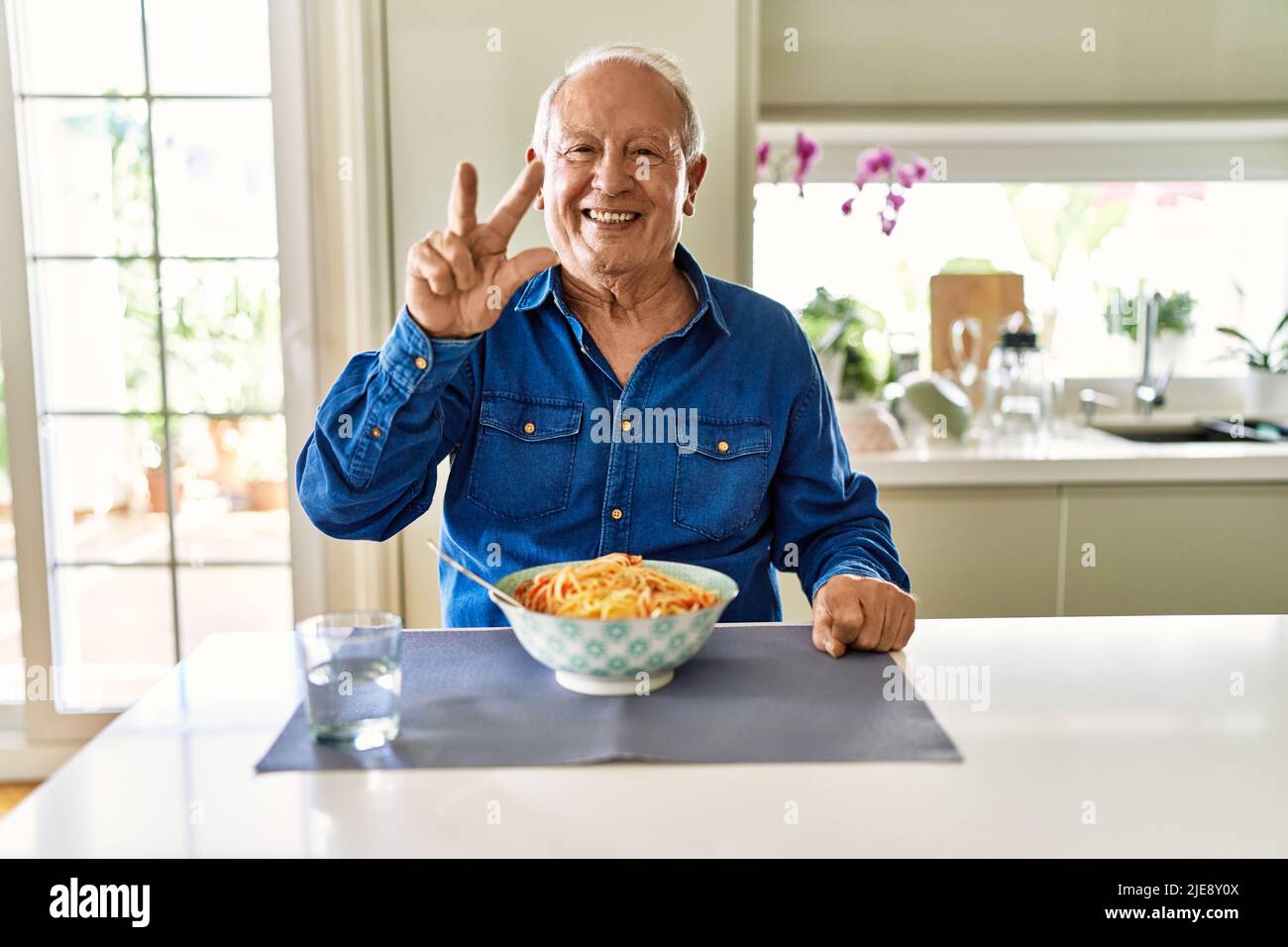 Senior man with grey hair eating pasta spaghetti at home showing and ...