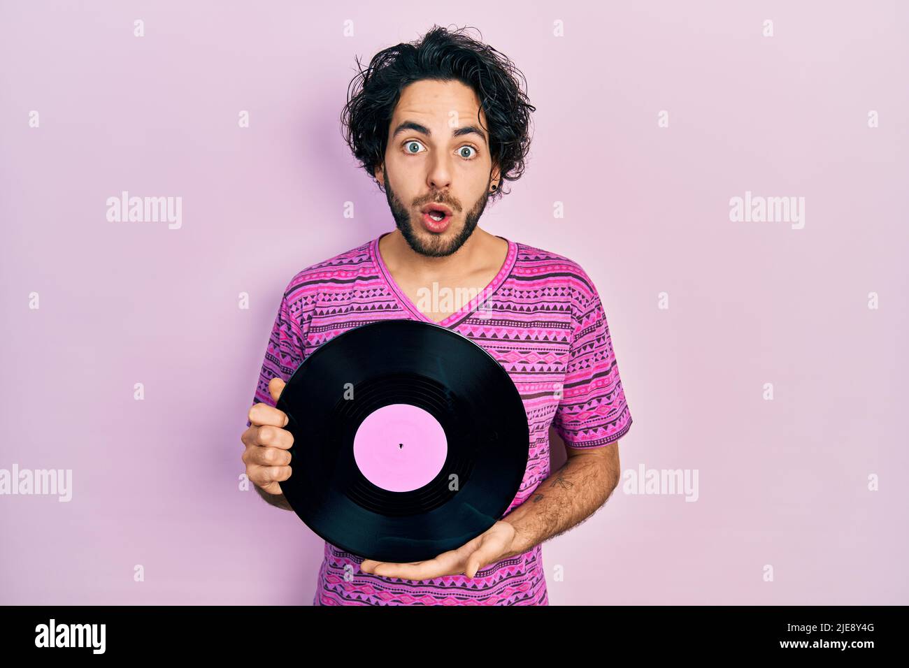 Handsome hispanic man holding vinyl disc afraid and shocked with ...