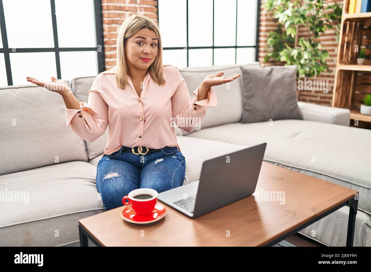 Young hispanic woman using laptop sitting on the sofa at home clueless ...