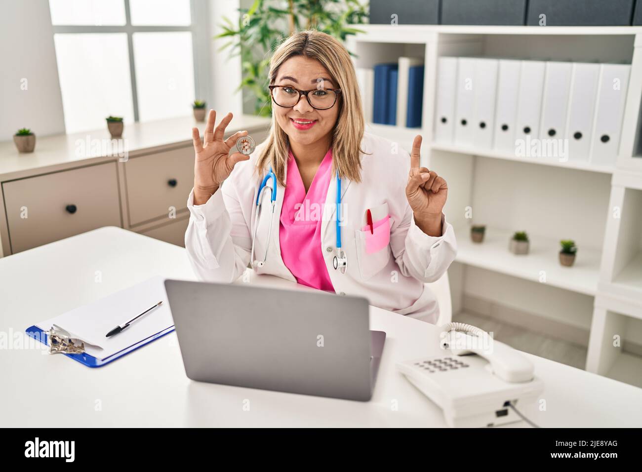 Young hispanic doctor woman holding virtual currency bitcoin smiling ...