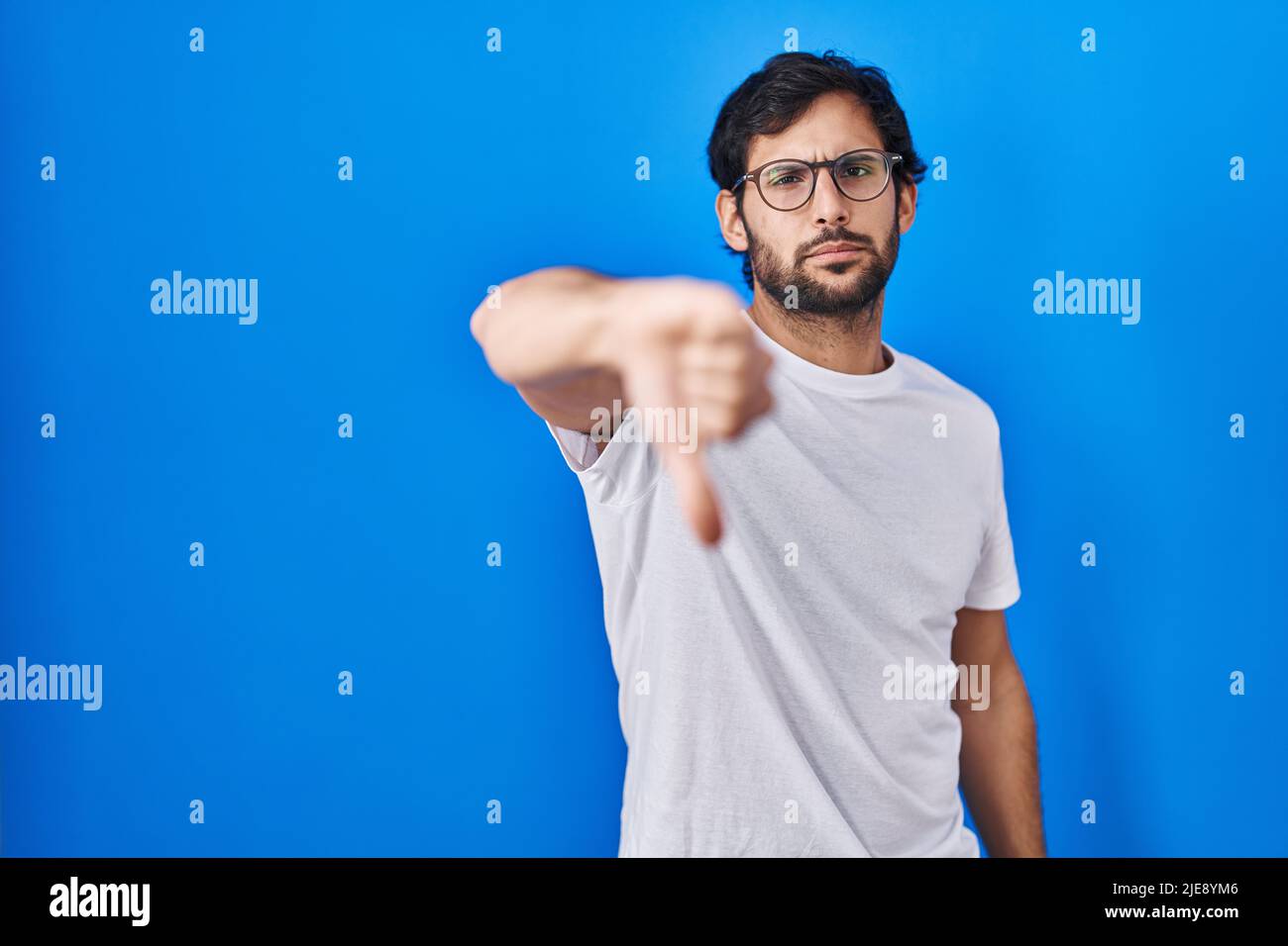 Handsome latin man standing over blue background looking unhappy and ...
