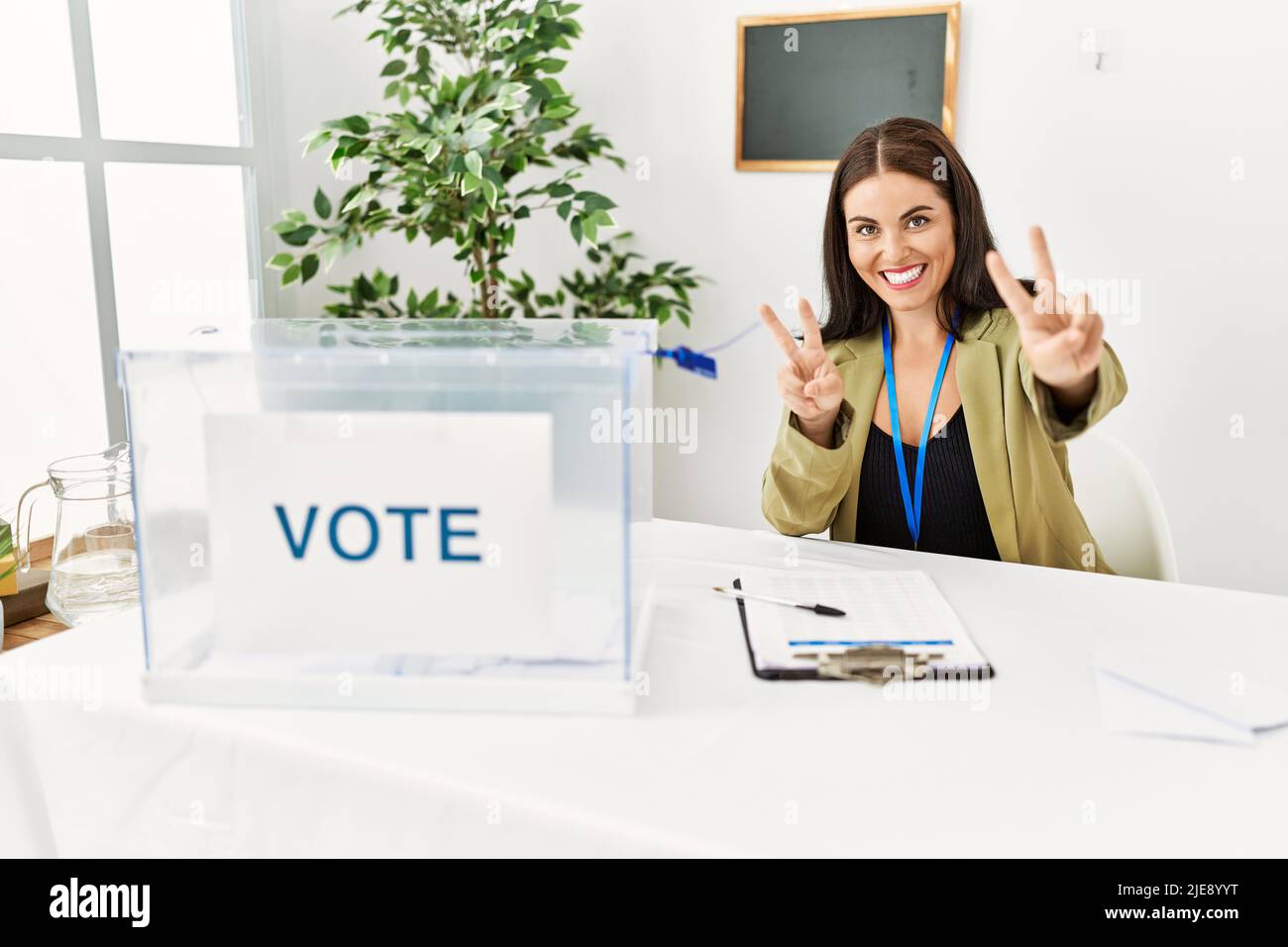 Young brunette woman sitting at election table with voting ballot ...
