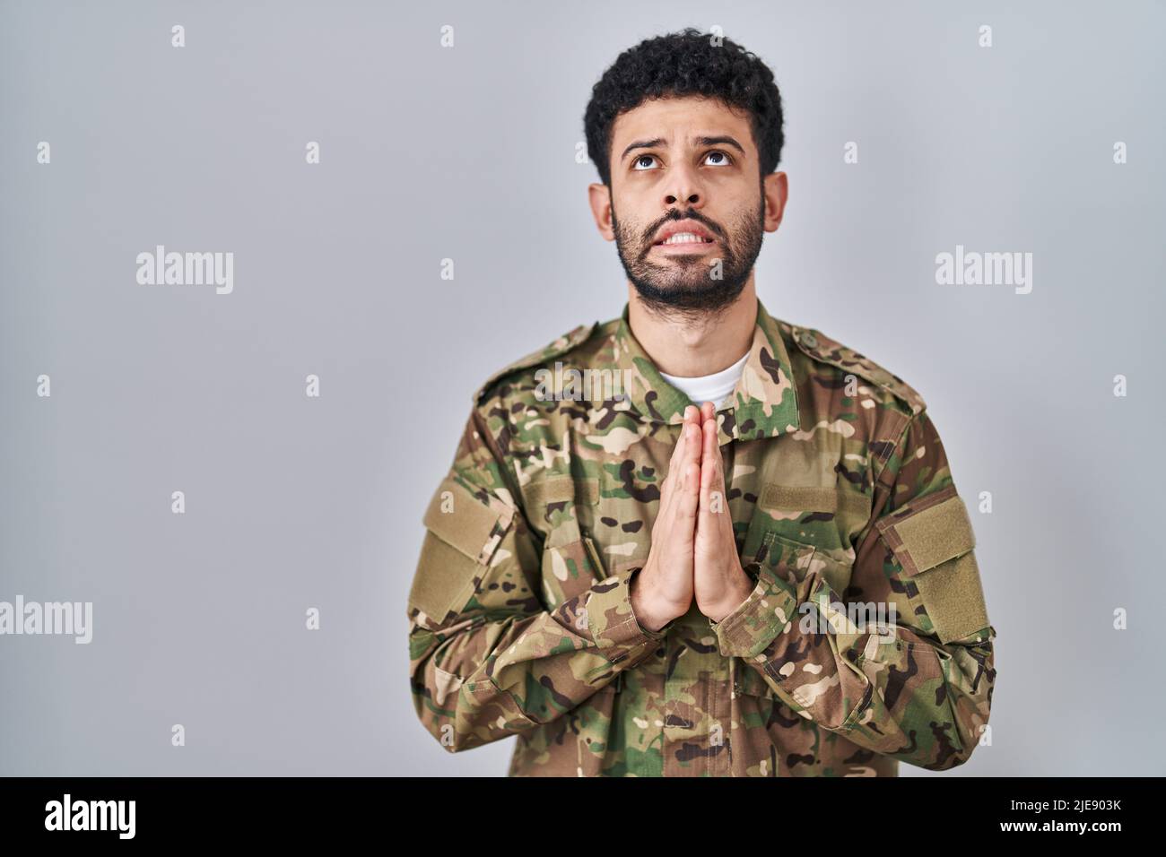 Arab man wearing camouflage army uniform begging and praying with hands ...