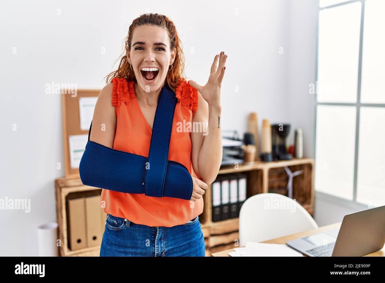 Young redhead woman wearing arm on sling at the office celebrating ...