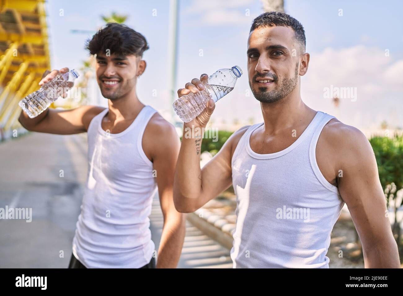 Two hispanic men sporty couple smiling confident drinking water at ...