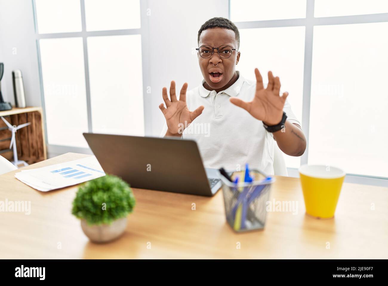 Young african man working at the office using computer laptop afraid ...
