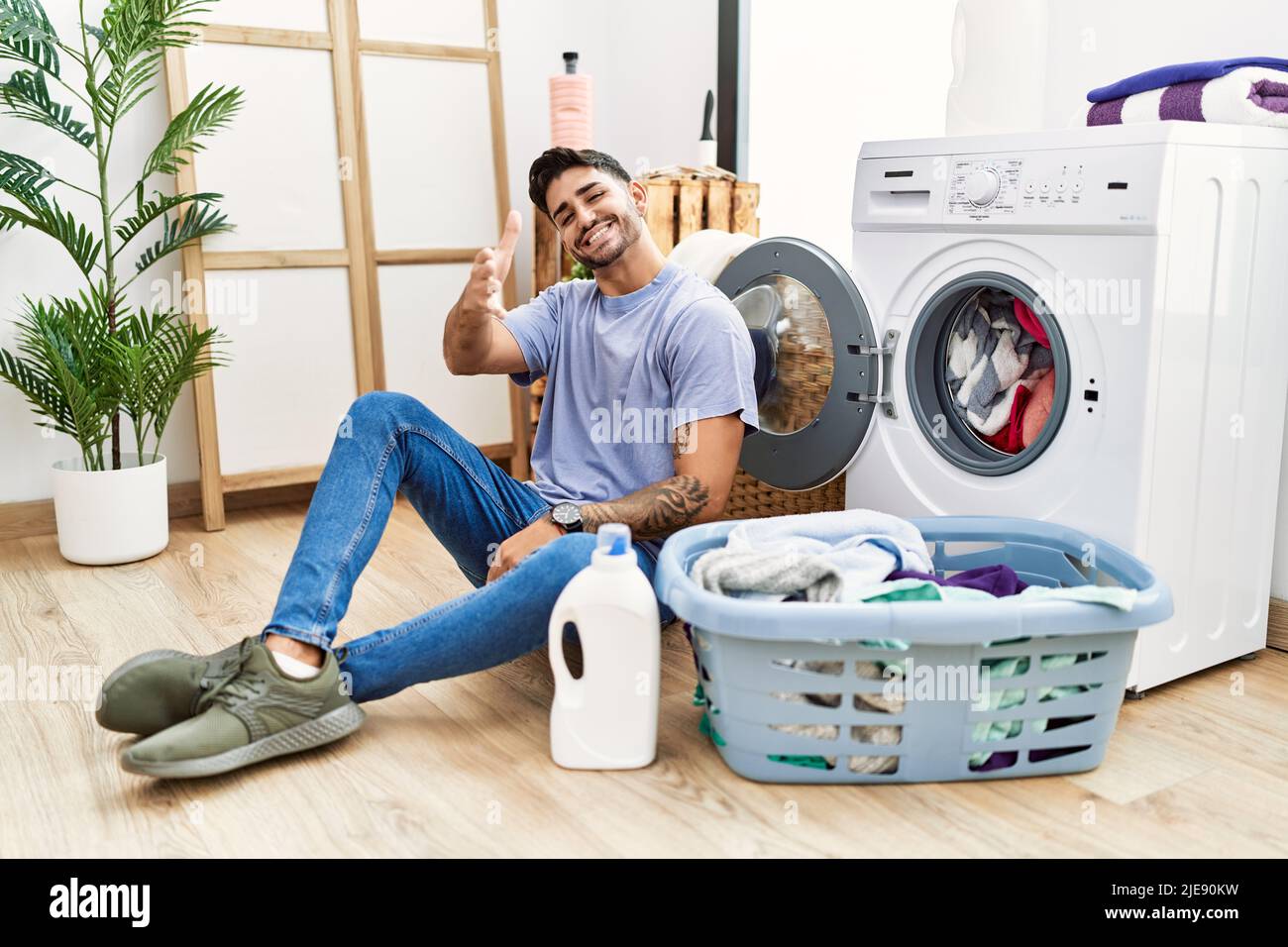 Young hispanic man putting dirty laundry into washing machine smiling ...