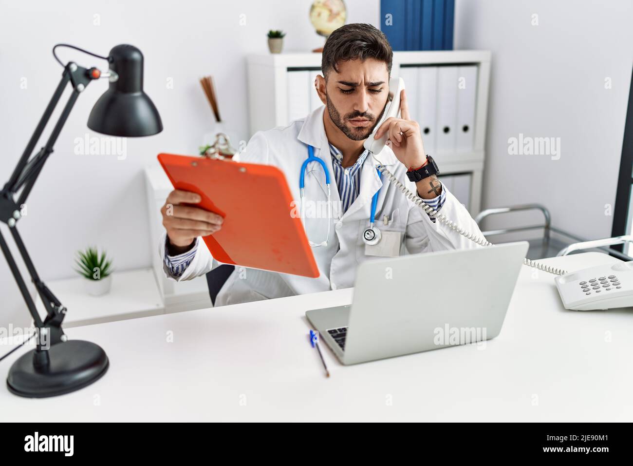 Handsome hispanic man working as doctor speaking on the phone at ...