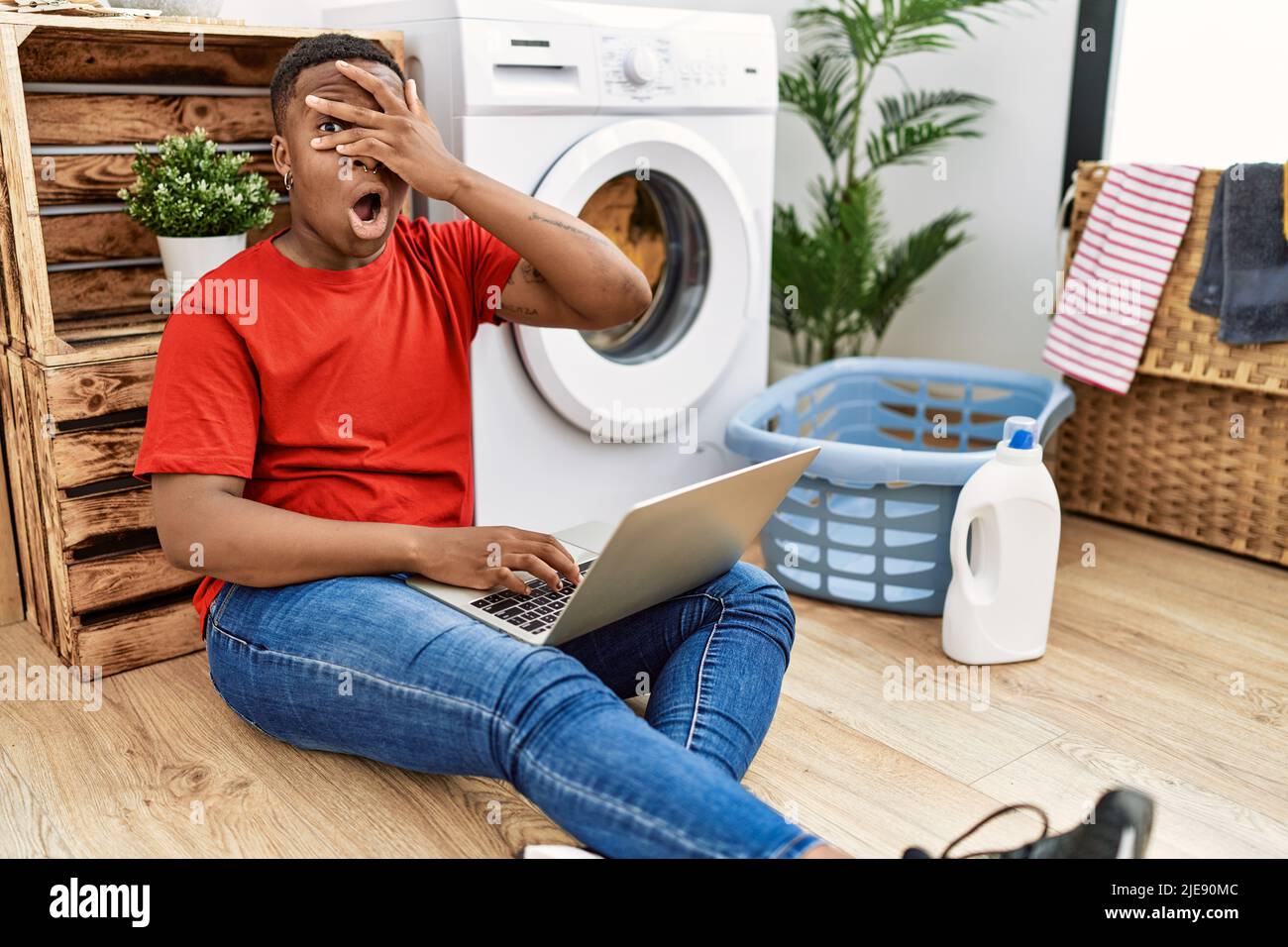 Young african man doing laundry and using computer peeking in shock ...