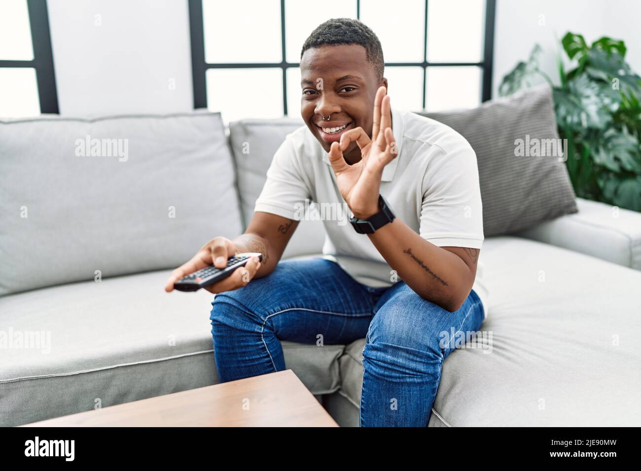 Young african man watching tv holding television remote control doing ...