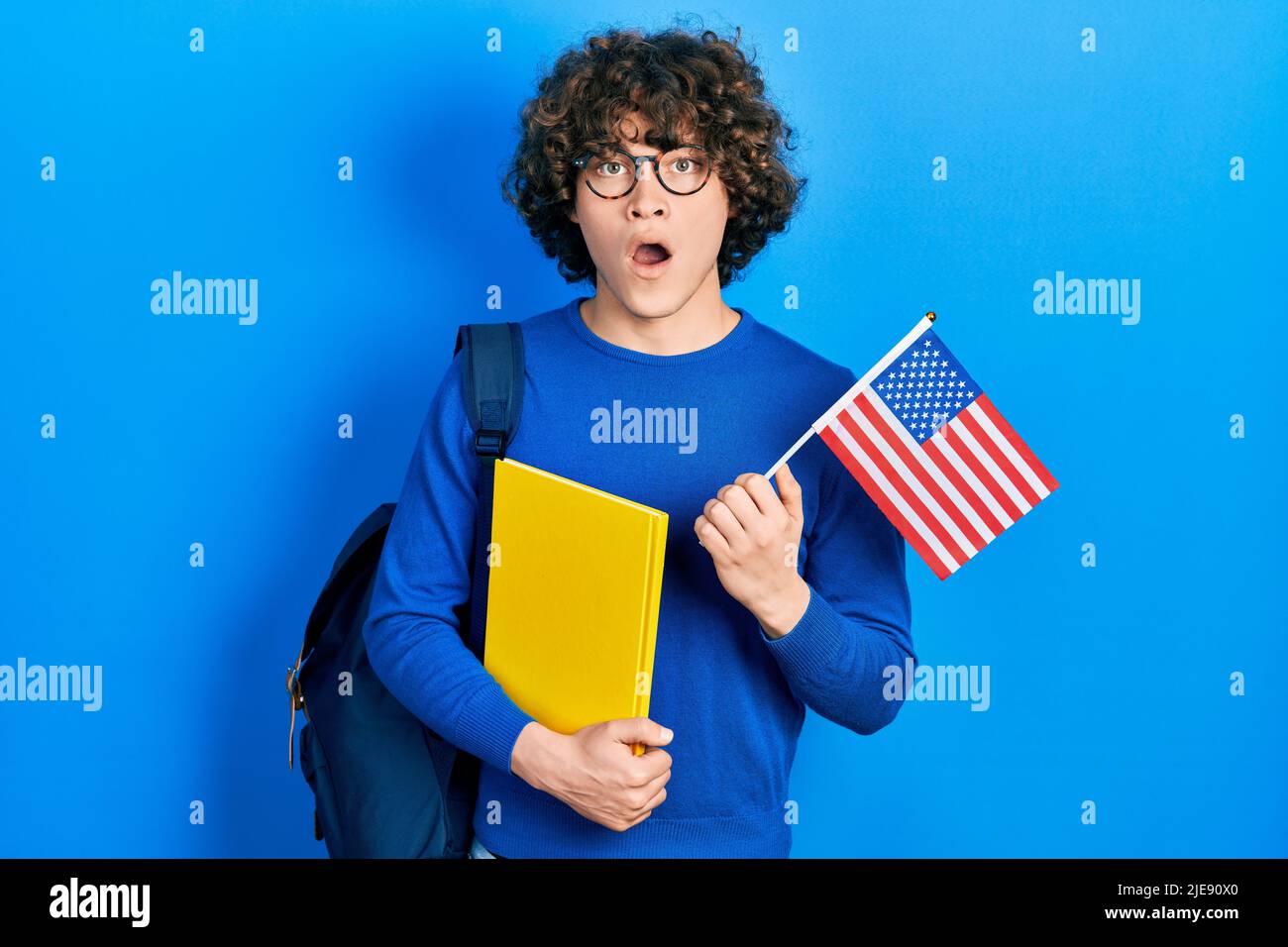 Handsome young man exchange student holding usa flag afraid and shocked ...