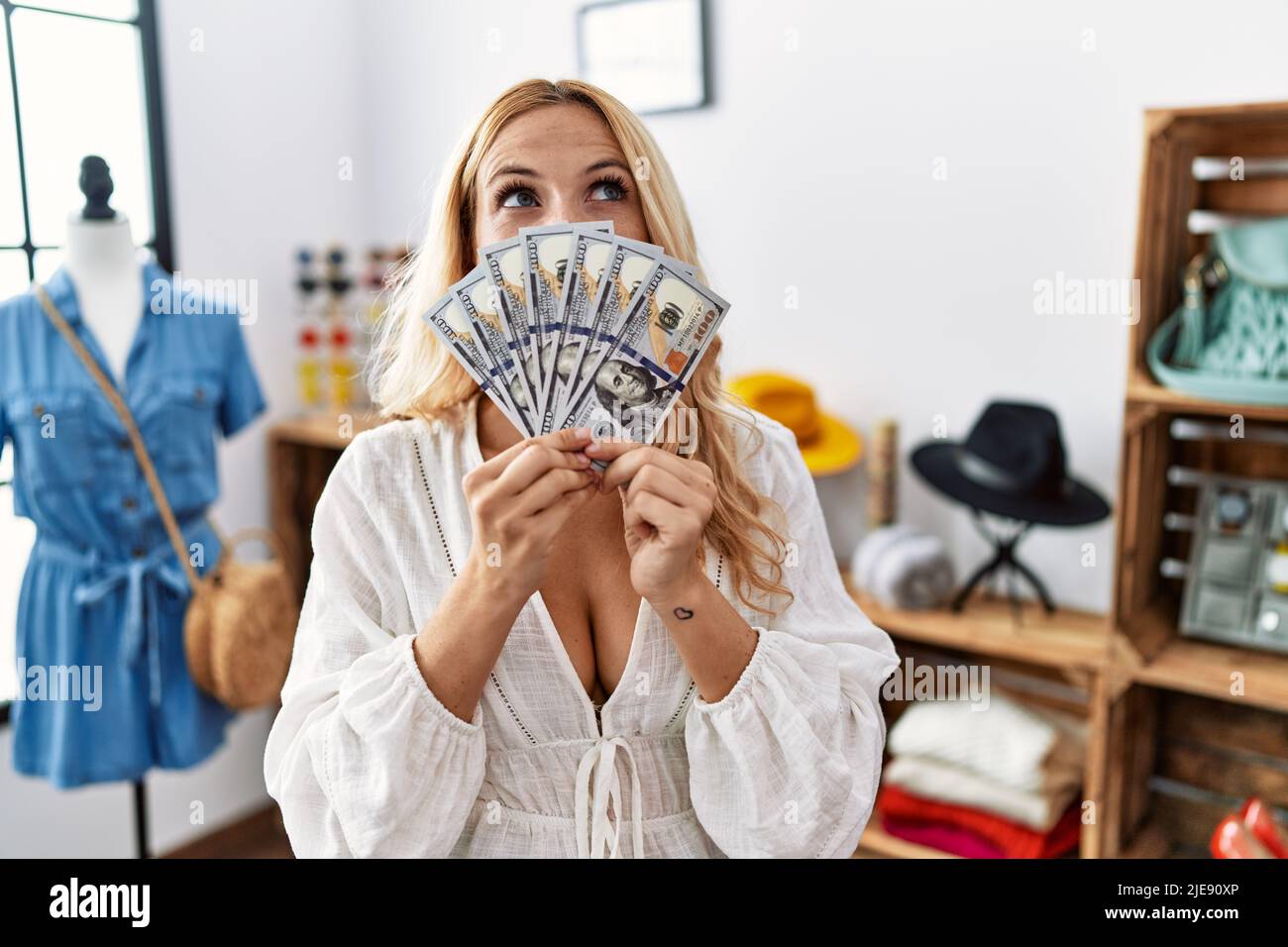 Beautiful blonde woman at retail boutique holding dollars banknotes ...