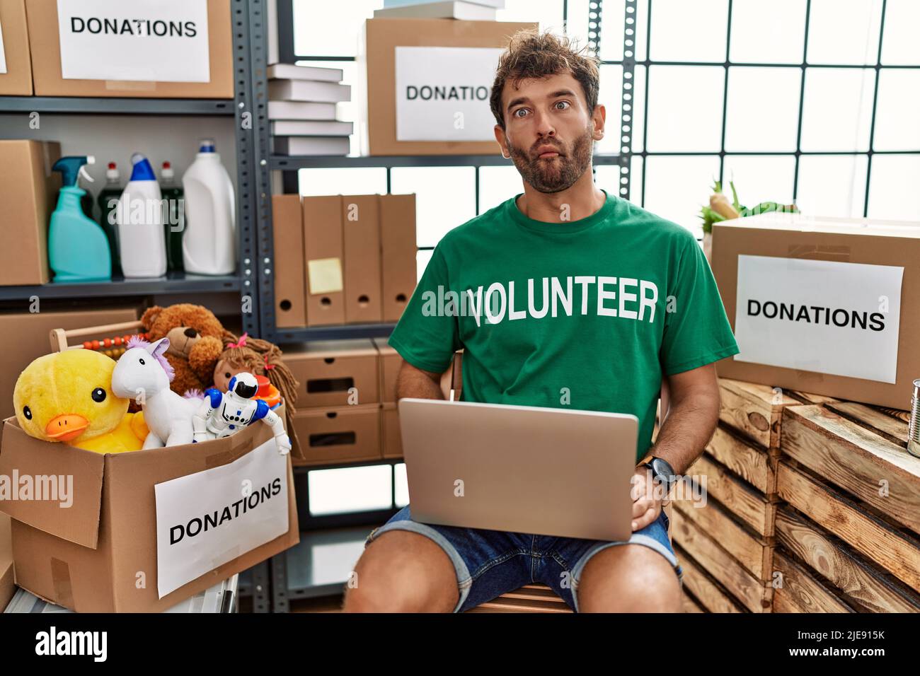 Young handsome man wearing volunteer t shirt using laptop making fish ...