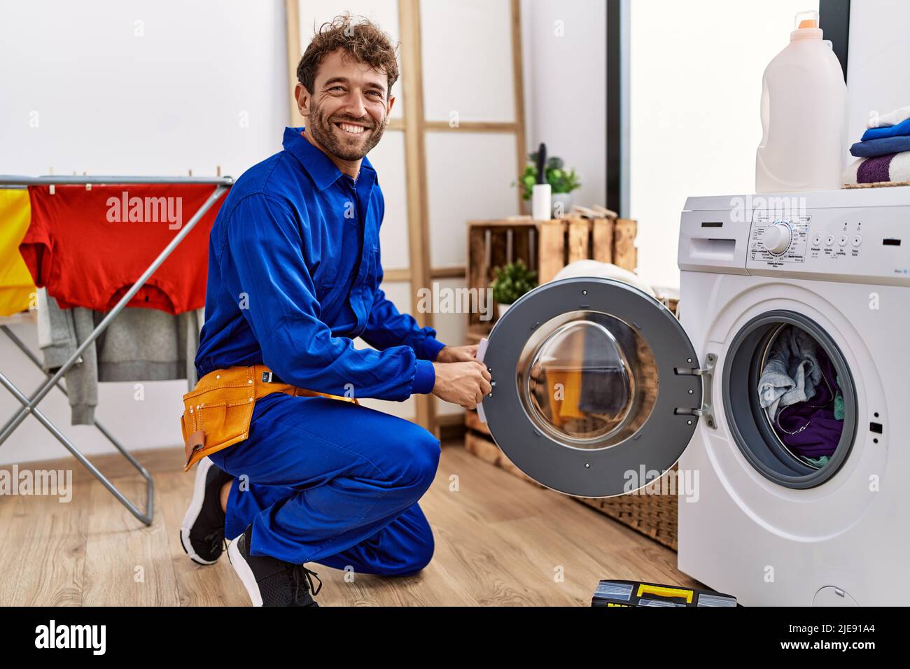 Young hispanic man wearing handyman uniform repairing washing machine ...