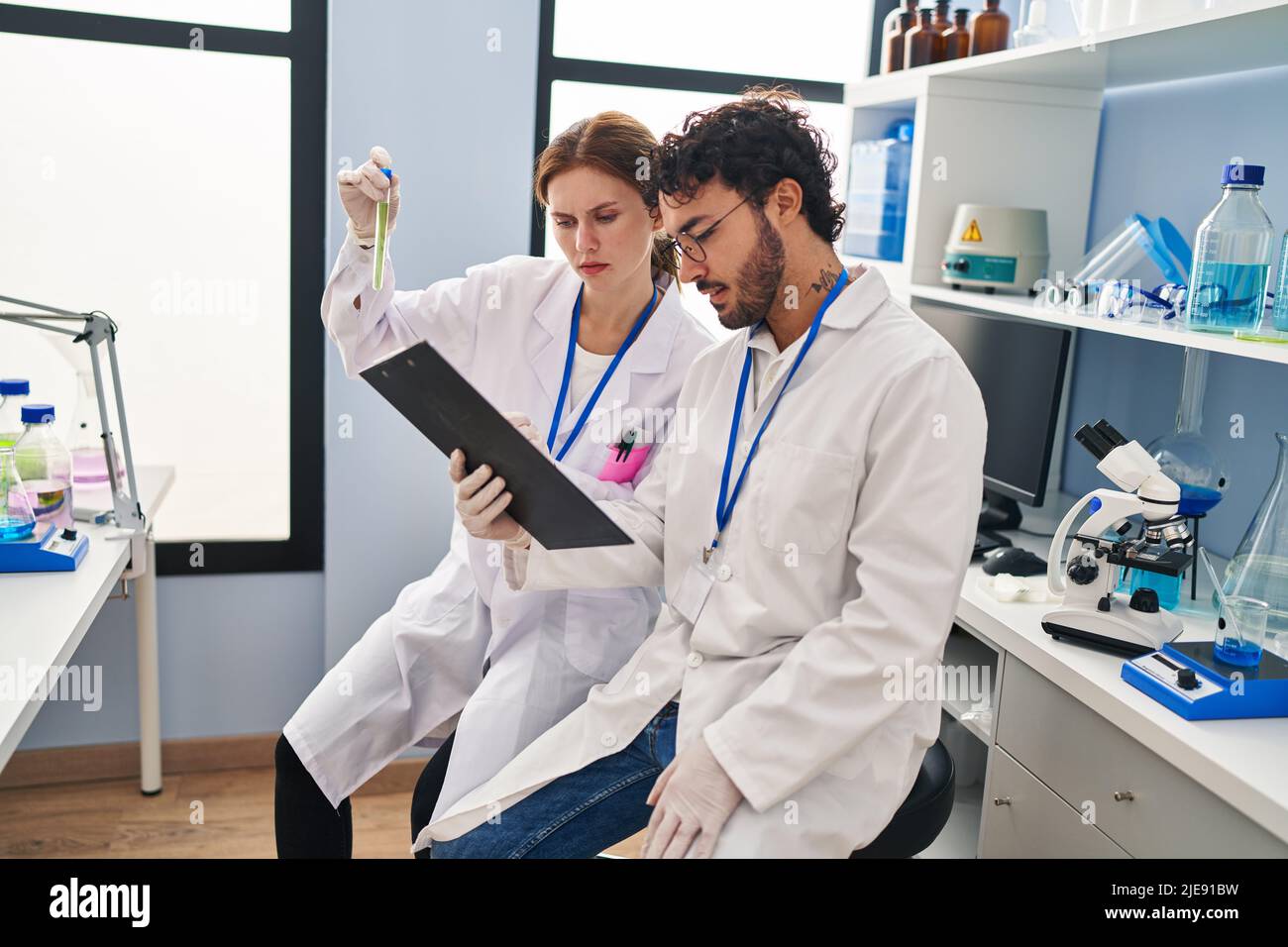 Man and woman scientist partners looking test tube holding clipboard at ...