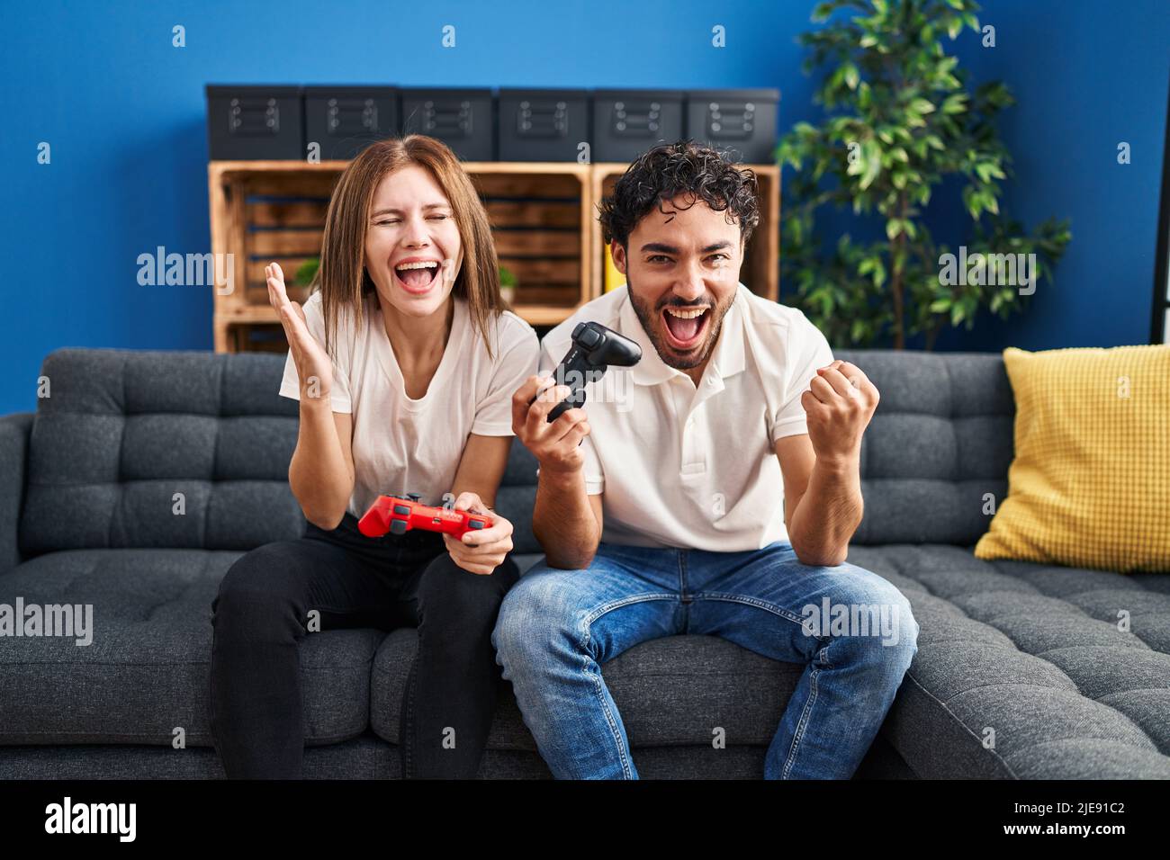 Young couple playing video game holding controller at home celebrating ...