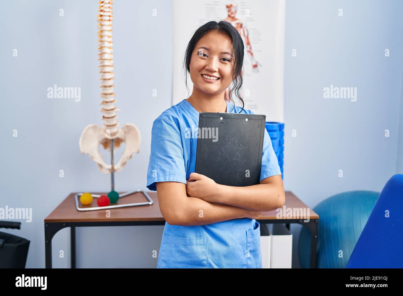Young chinese woman wearing physiotherapist uniform holding clipboard ...