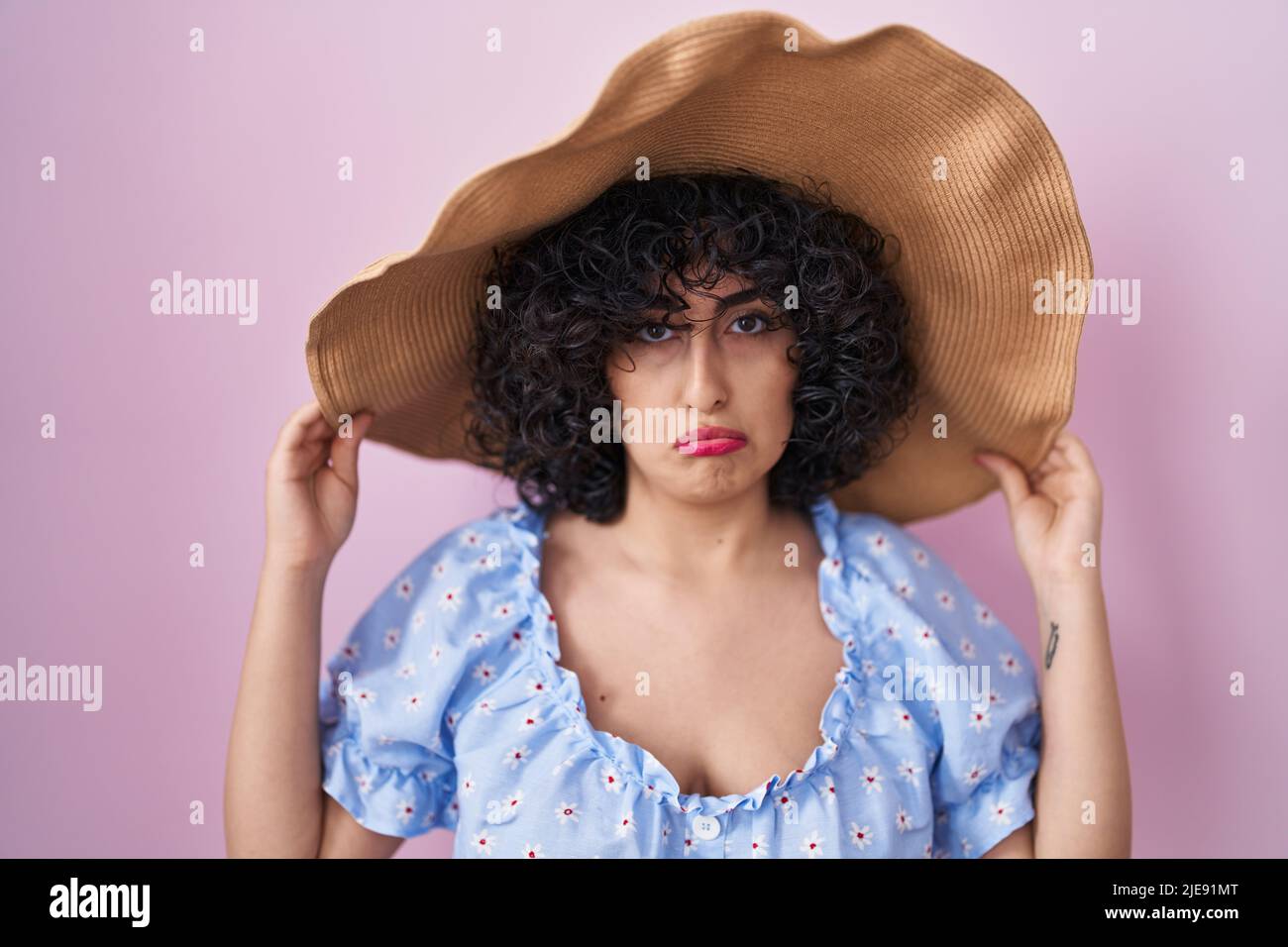Young brunette woman with curly hair wearing summer hat depressed and ...