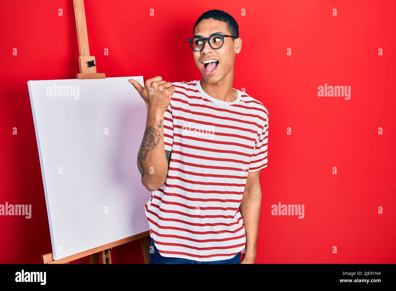 Young african american guy standing by painter easel stand pointing ...