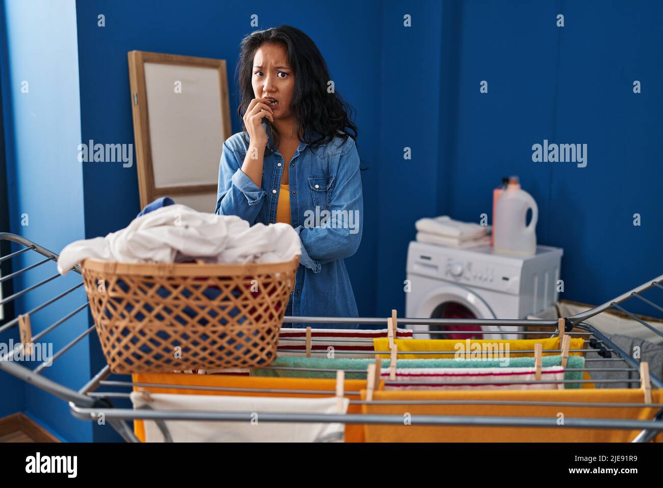 Young asian woman hanging clothes at clothesline looking stressed and ...