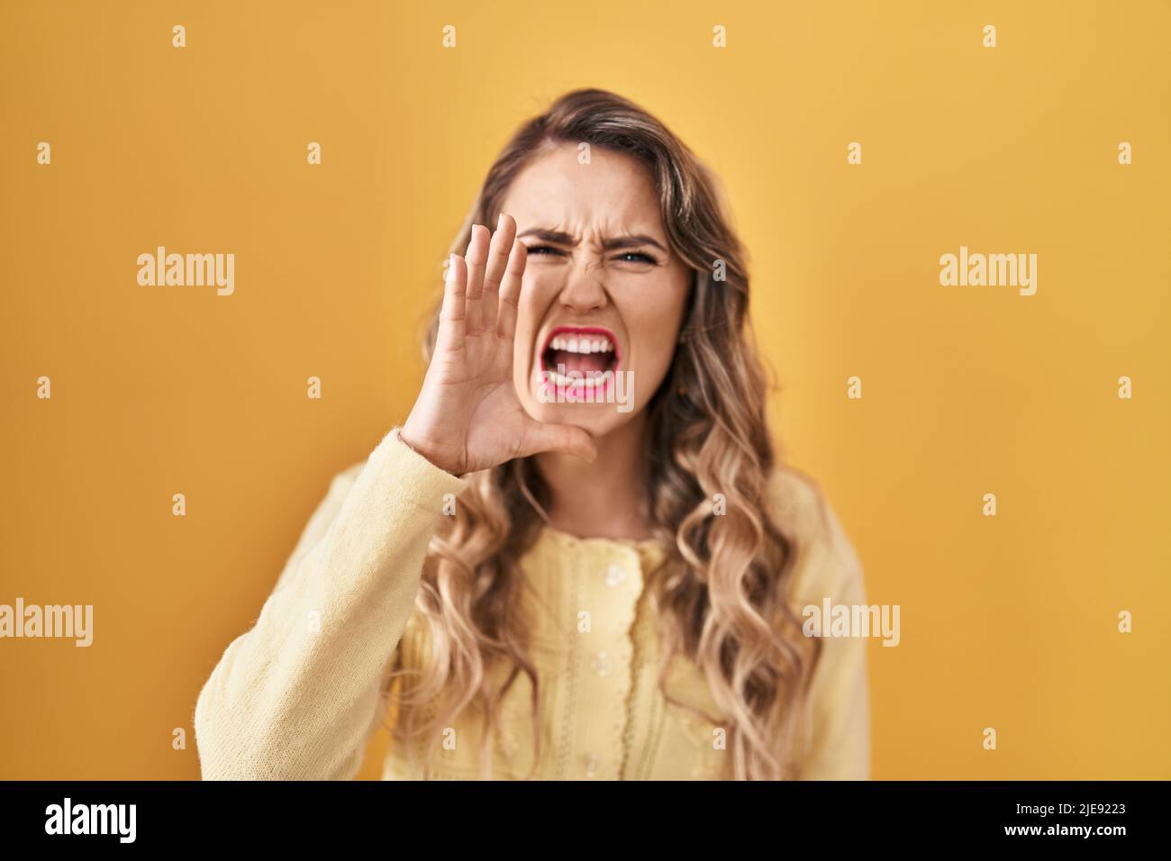 Young caucasian woman standing over yellow background shouting and ...