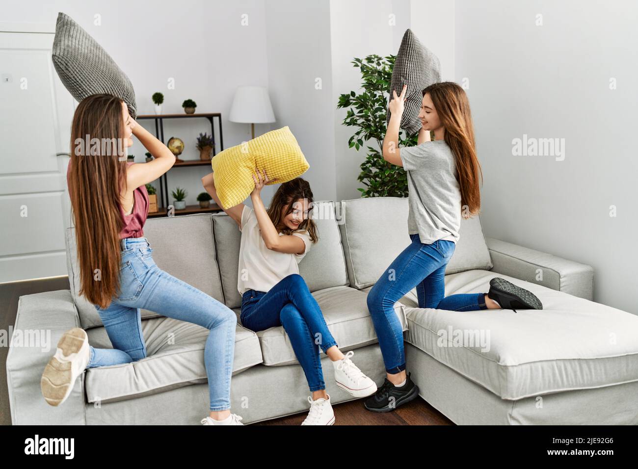 Three young hispanic woman smiling happy fighting with pillowa at home ...