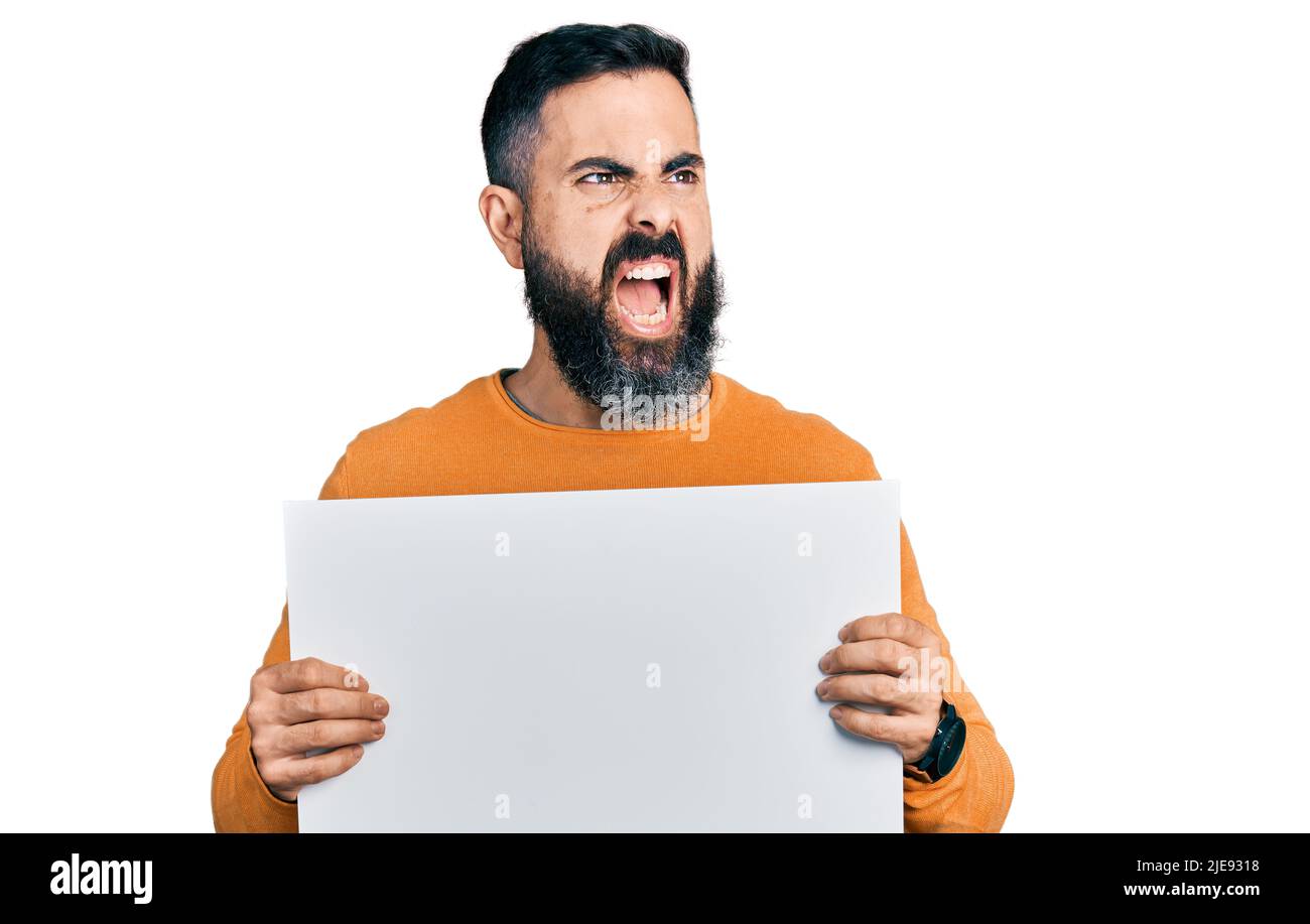 Hispanic man with beard holding blank empty banner angry and mad ...