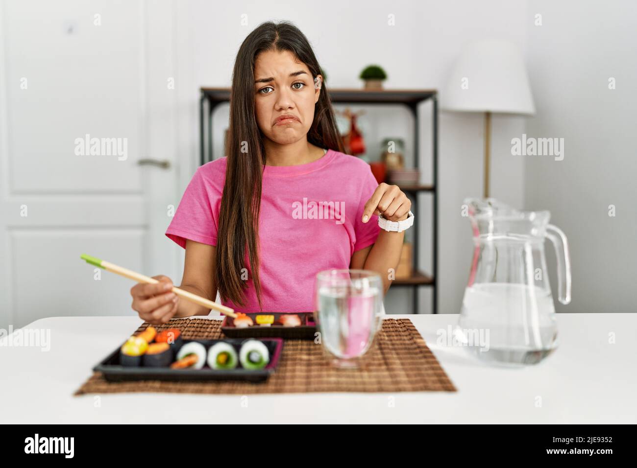 Young brunette woman eating sushi using chopsticks pointing down ...