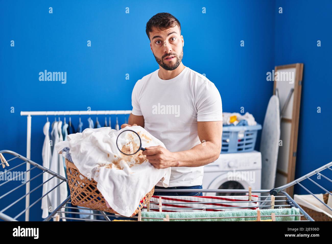 Handsome hispanic man holding magnifying glass looking for stain at ...