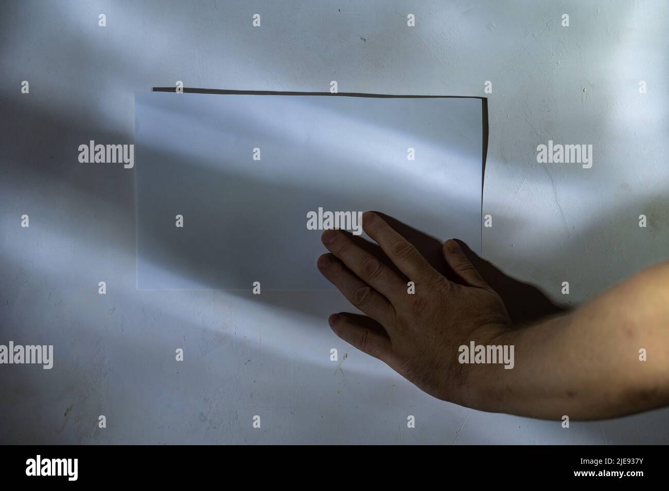 Hand of mature man presses sheet of paper against wall. Empty white ...