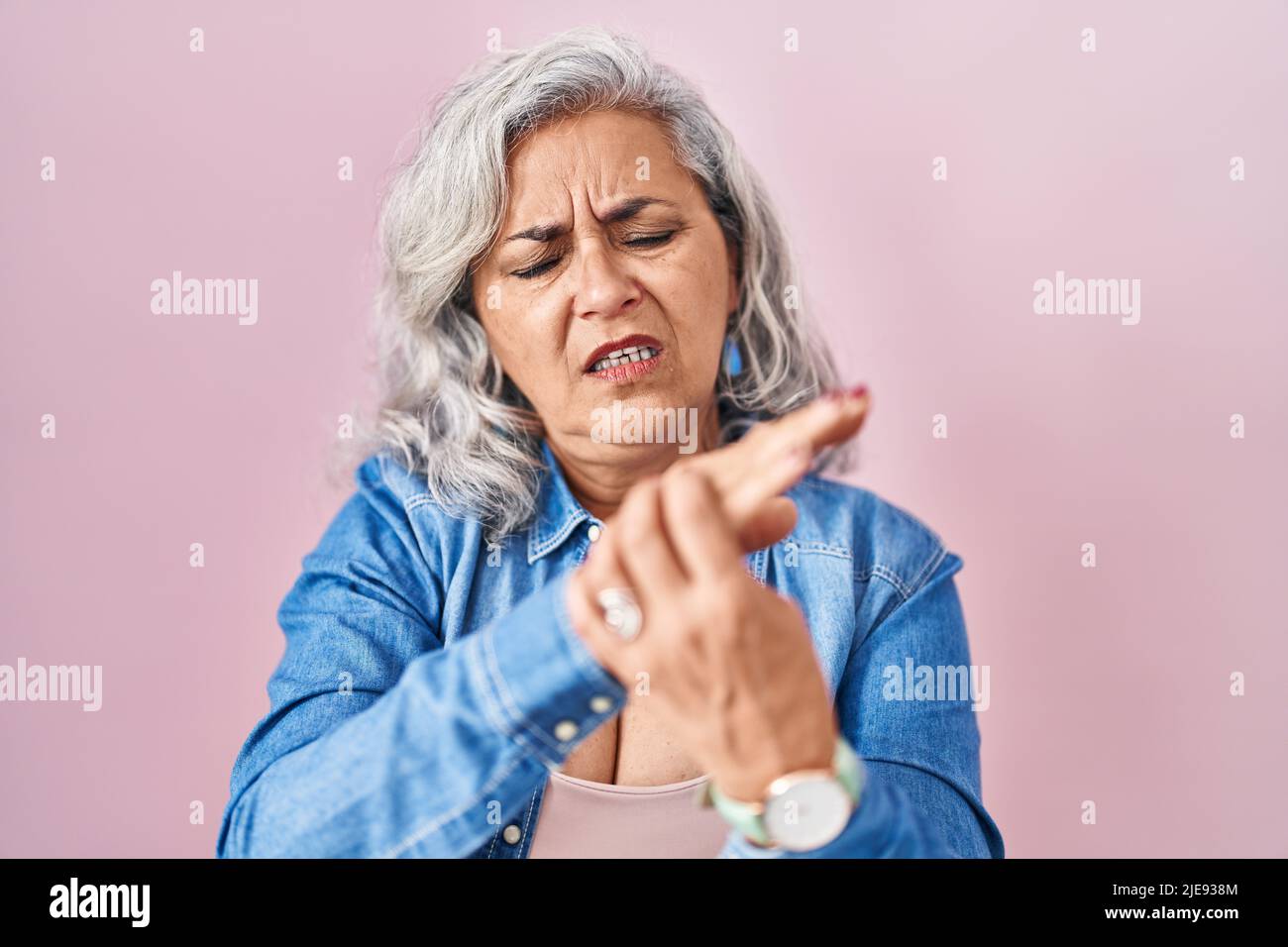 Middle age woman with grey hair standing over pink background suffering ...
