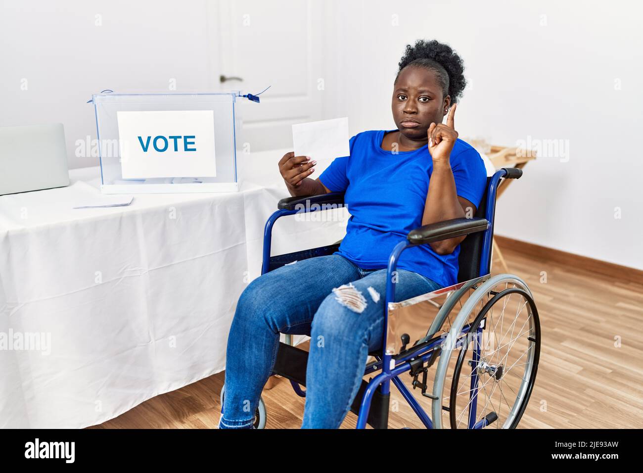 Young african woman sitting on wheelchair voting putting envelop in ...