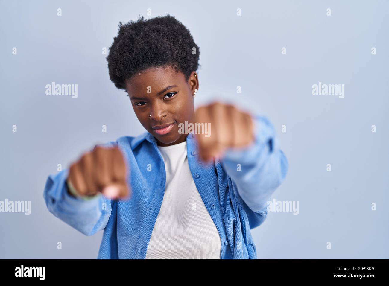 African american woman standing over blue background punching fist to ...