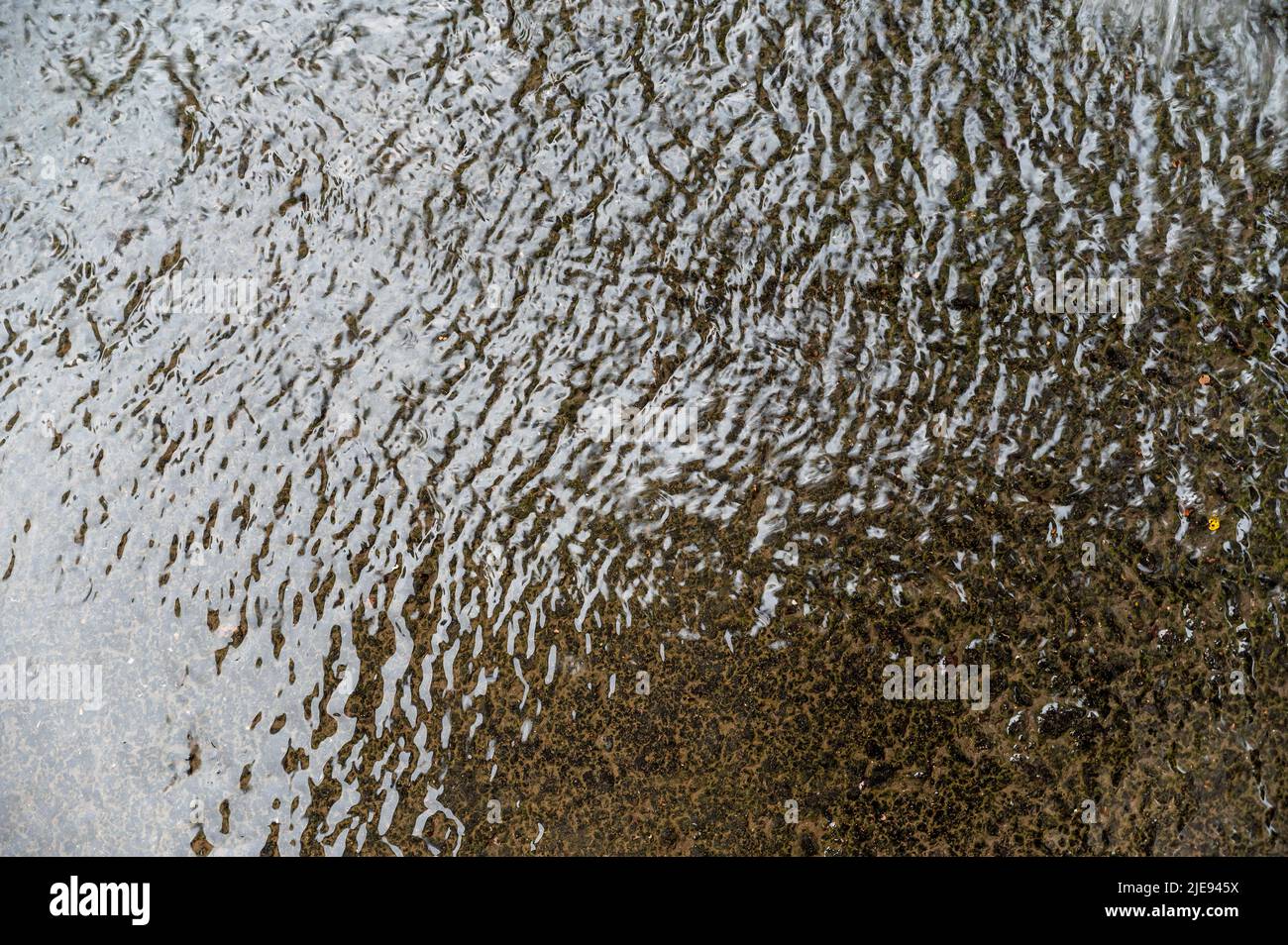 Texture of rain stream on city street. Transparent rainwater flowing on ...