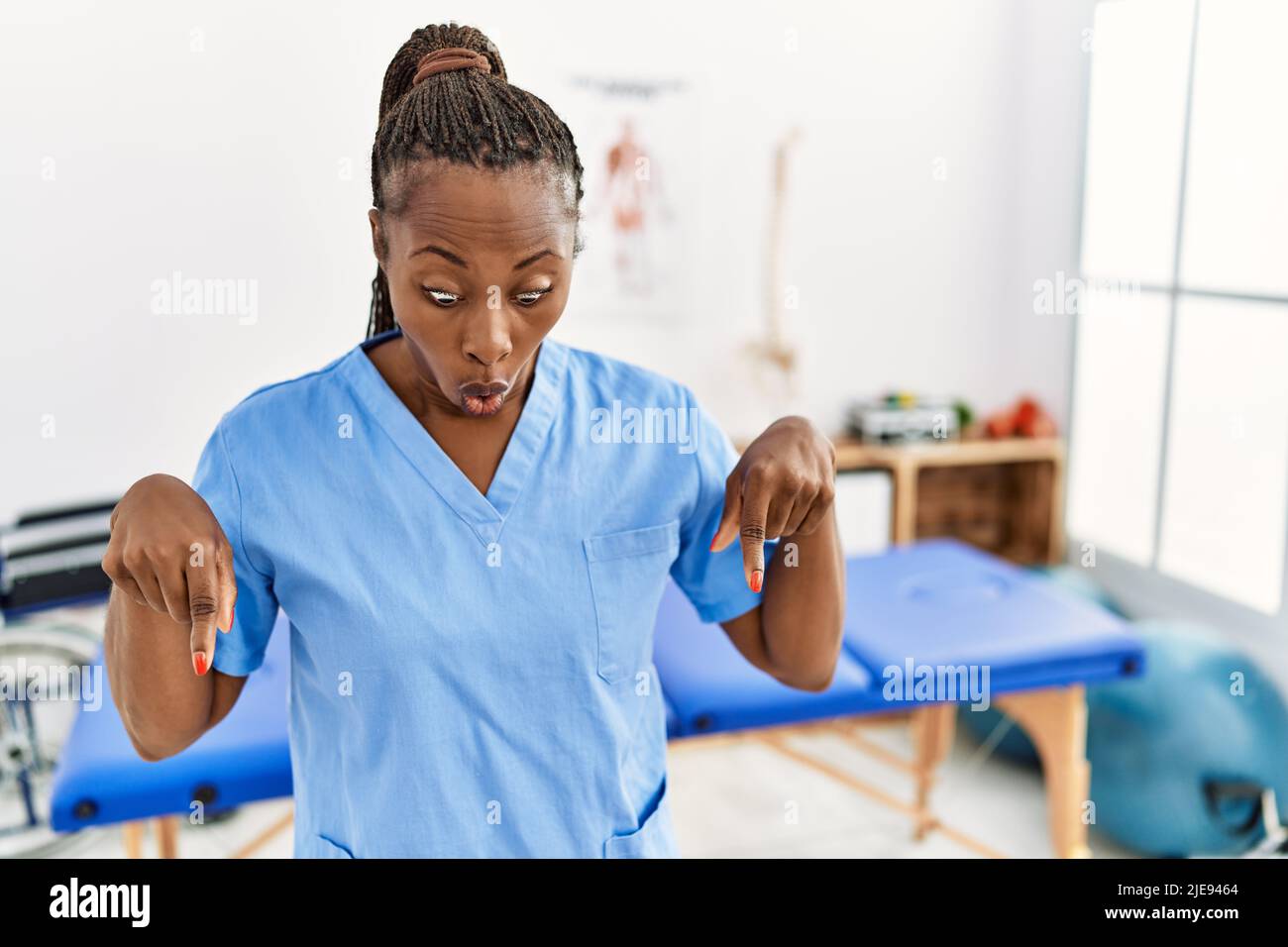 Black woman with braids working at pain recovery clinic pointing down ...
