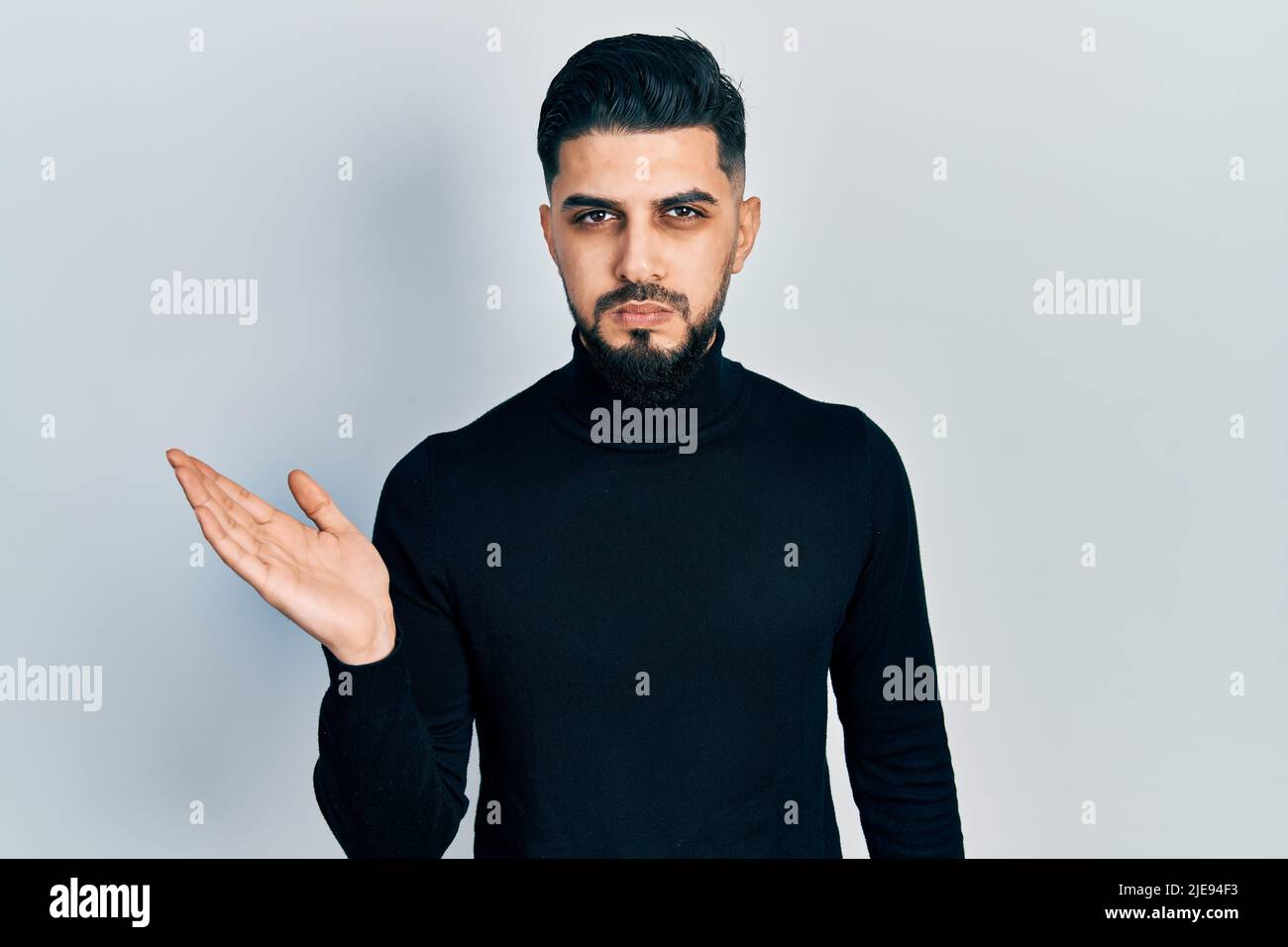 Handsome man with beard presenting with open palm puffing cheeks with ...