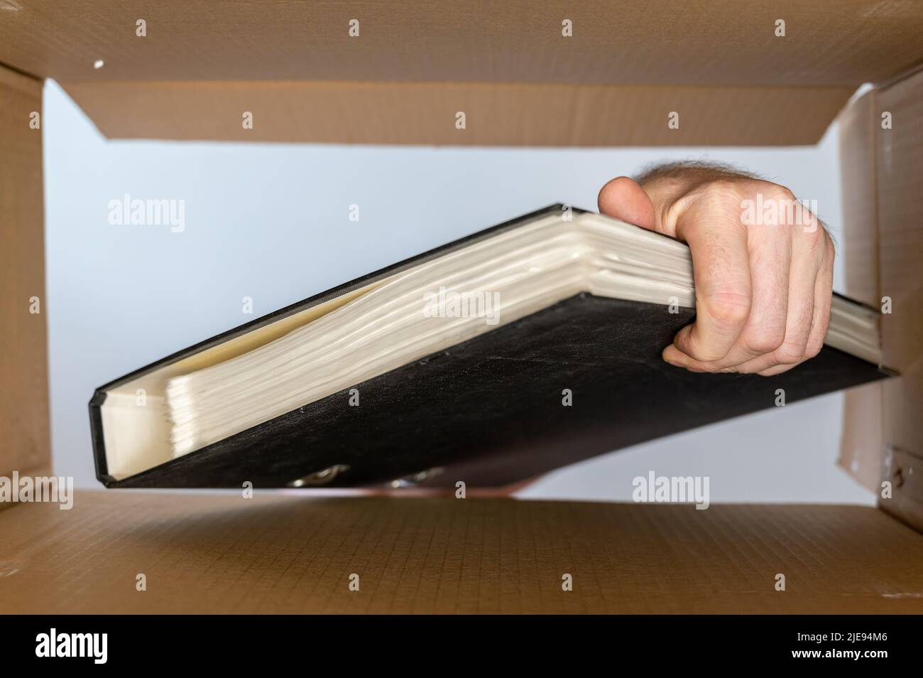 A man's hand pulls a ring binder folder out of a cardboard moving box ...