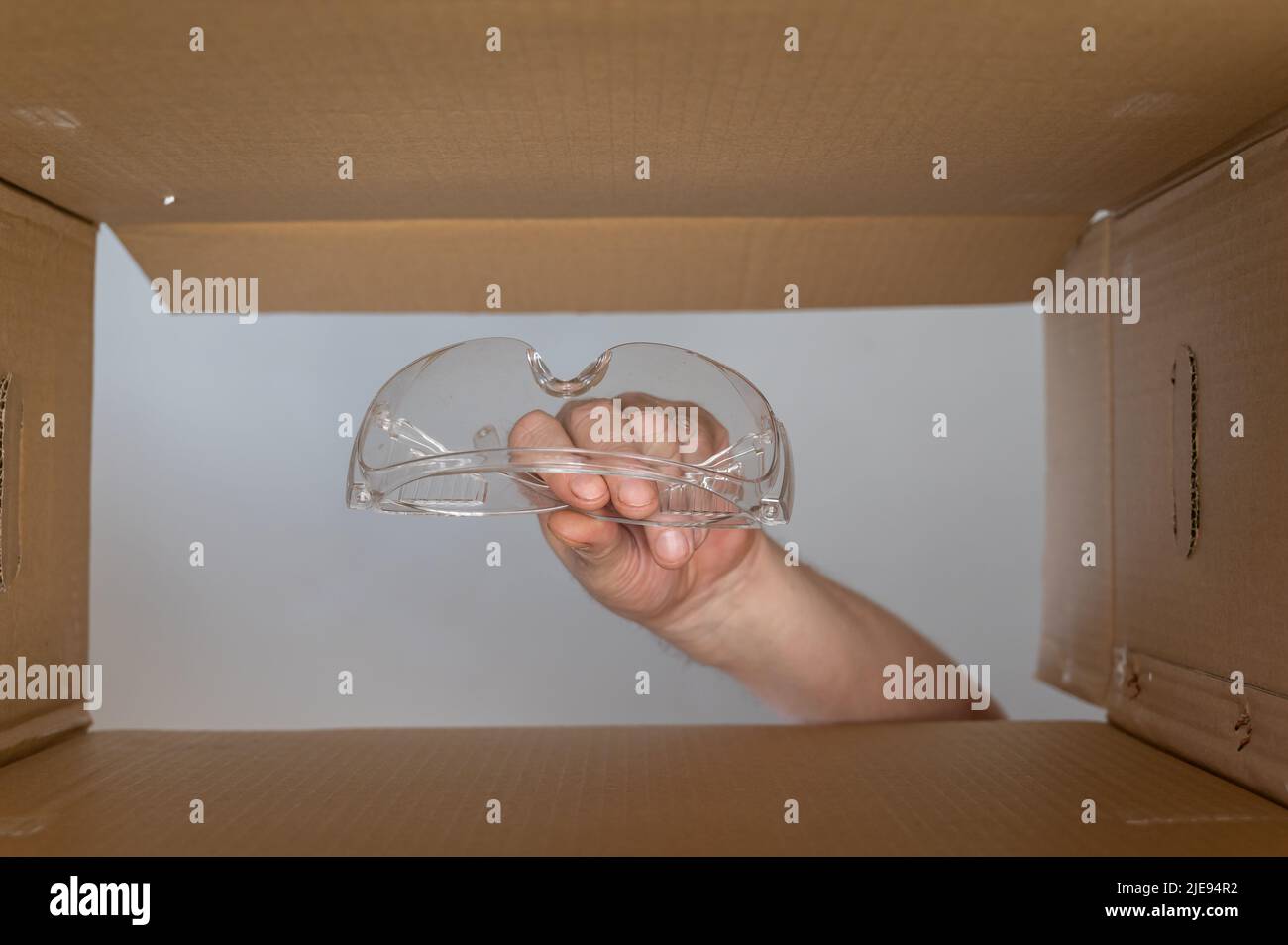 A man's hand puts safety glasses in a cardboard moving box. Plastic ...