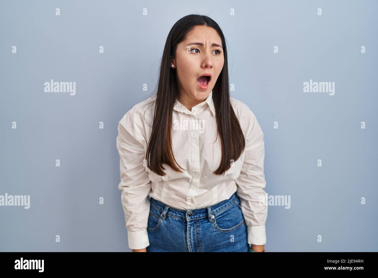Young latin woman standing over blue background angry and mad screaming ...