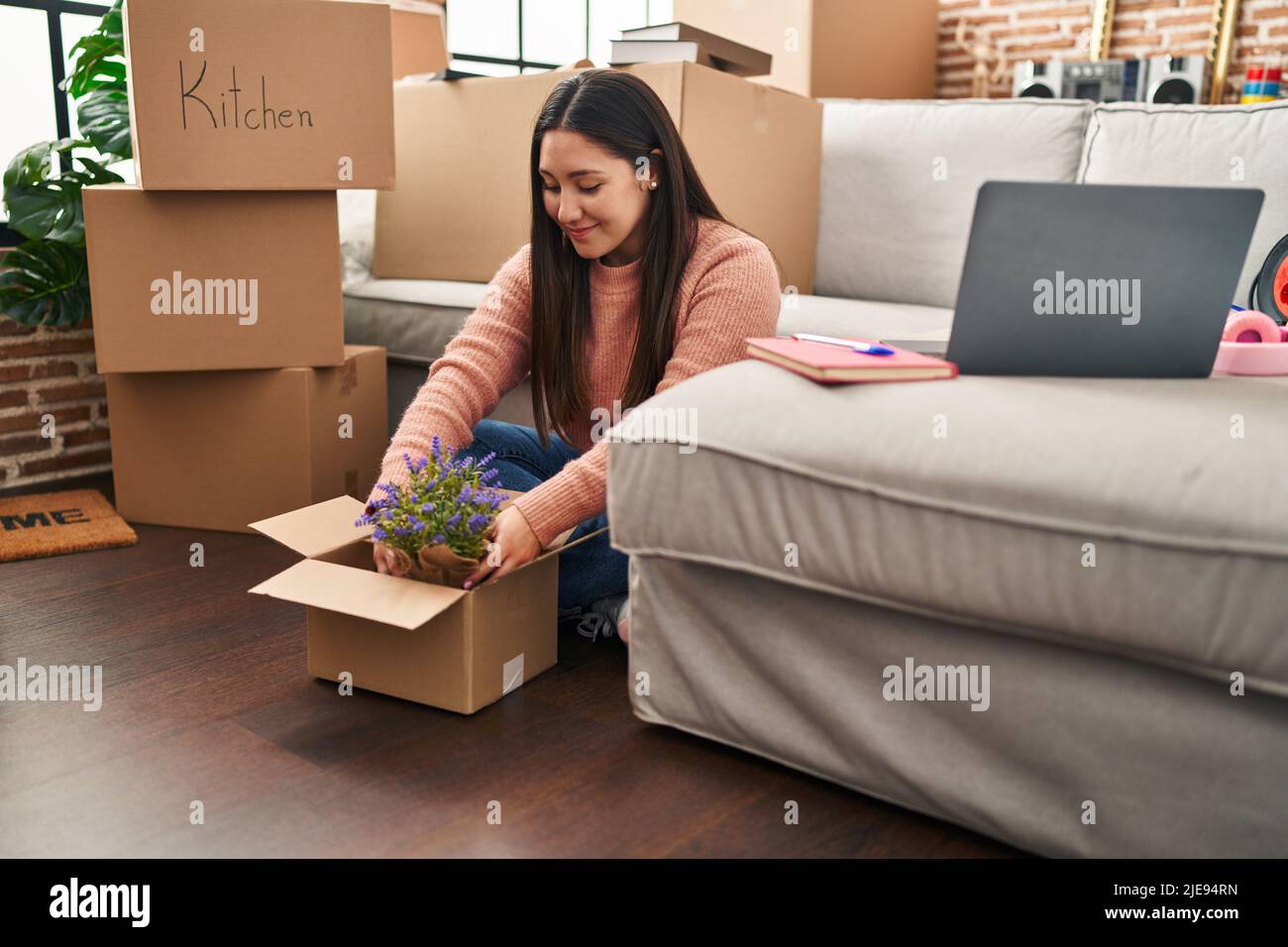Young hispanic woman unpacking lavander plant of cardboard box at new ...