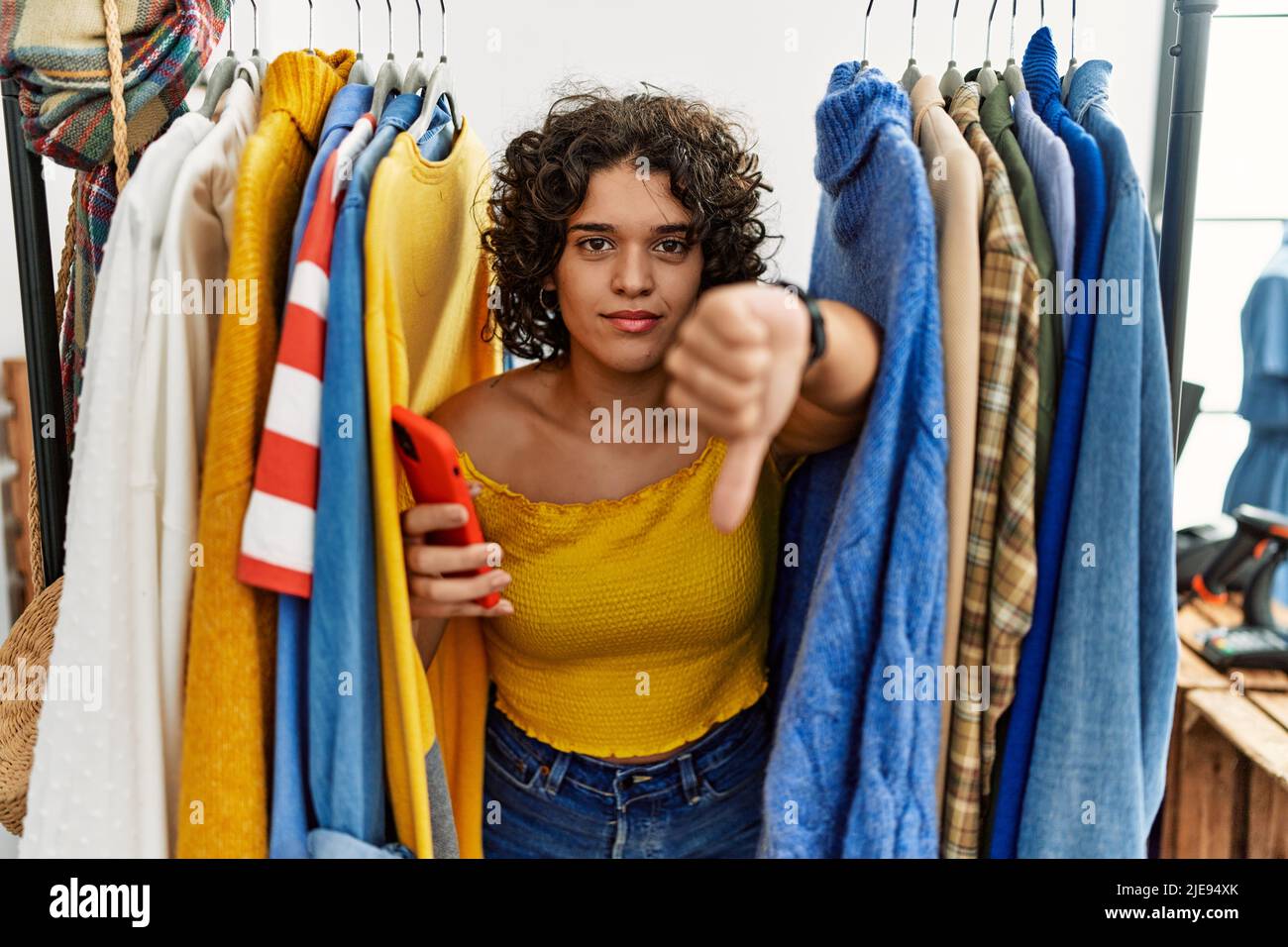 Young hispanic woman searching clothes on clothing rack using ...