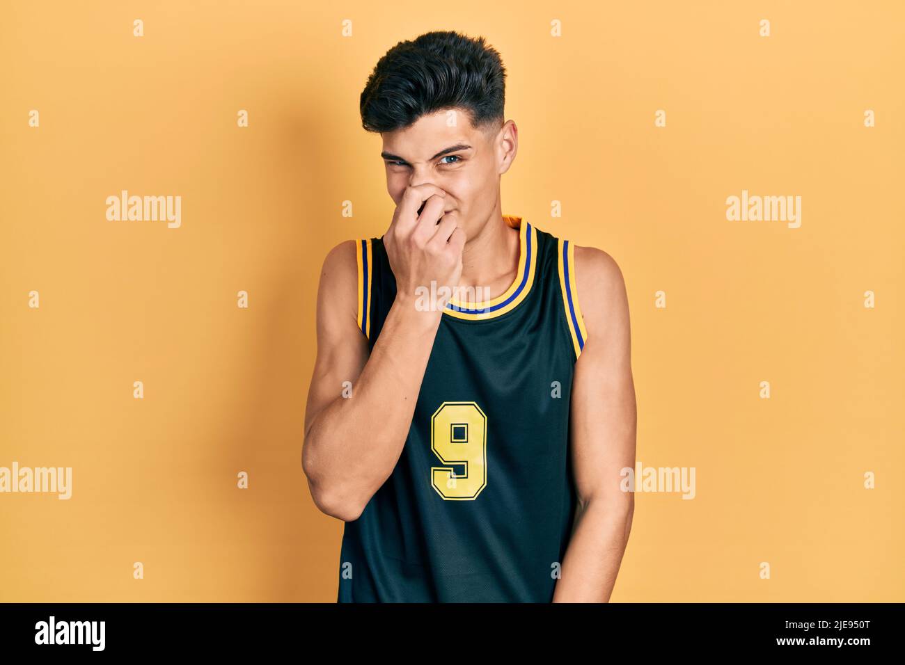 Young hispanic man wearing basketball uniform smelling something stinky ...
