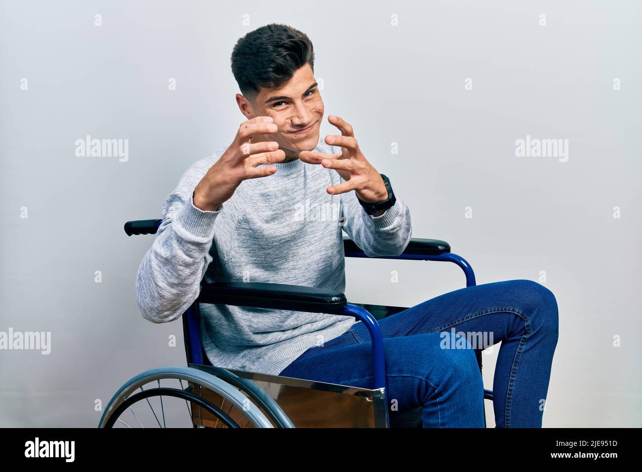 Young hispanic man sitting on wheelchair shouting frustrated with rage ...