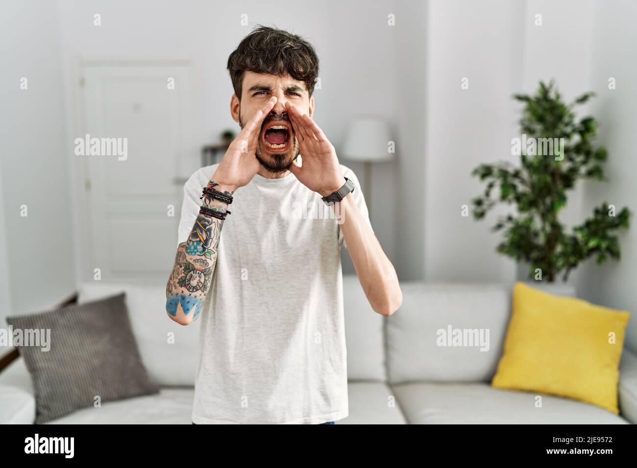 Hispanic man with beard at the living room at home shouting angry out ...