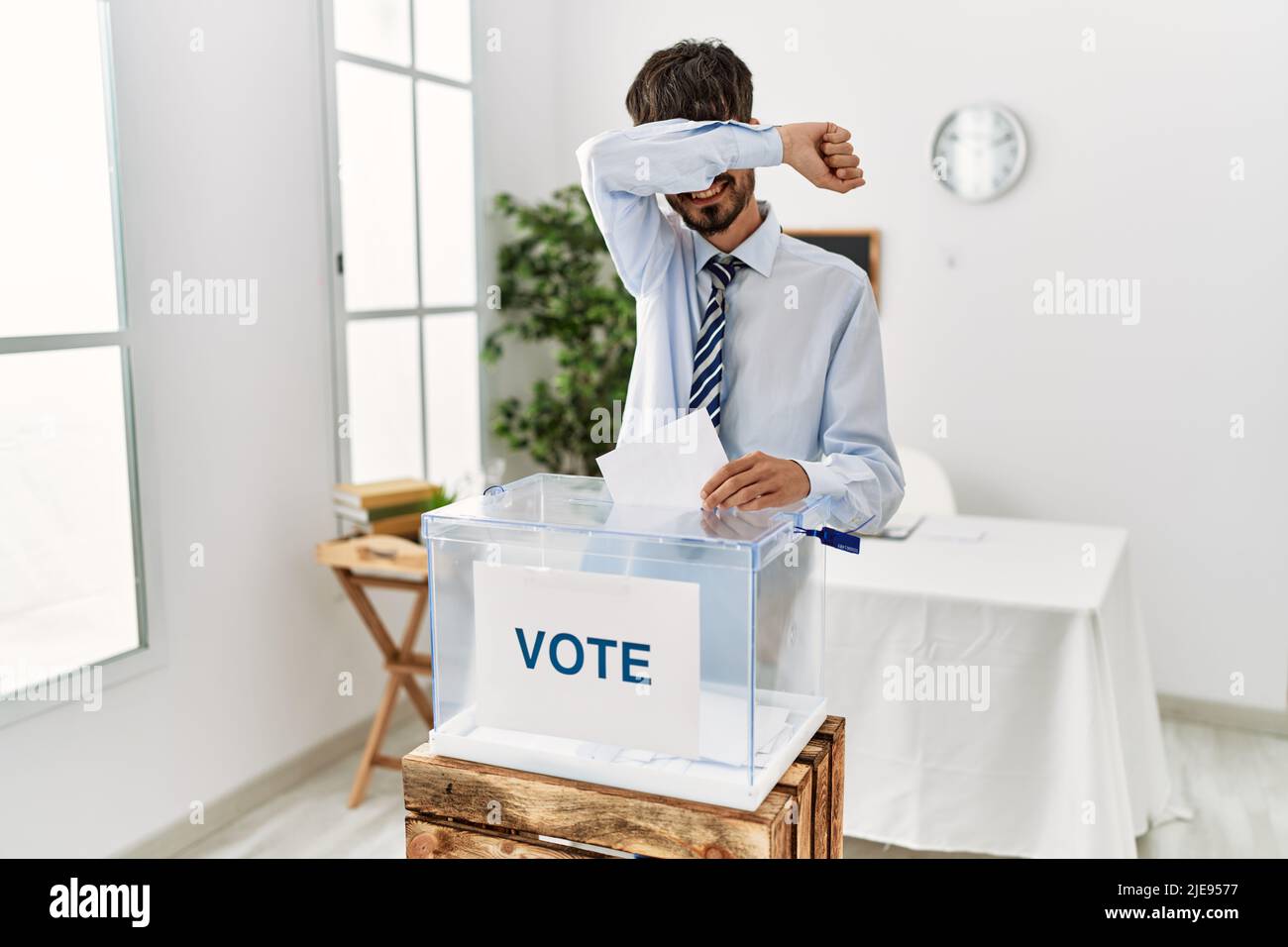 Hispanic man with beard voting putting envelop in ballot box smiling ...