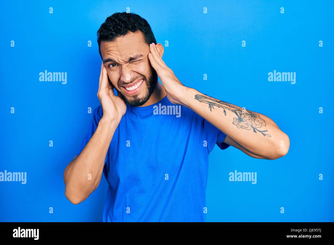 Hispanic man with beard wearing casual blue t shirt covering ears with ...