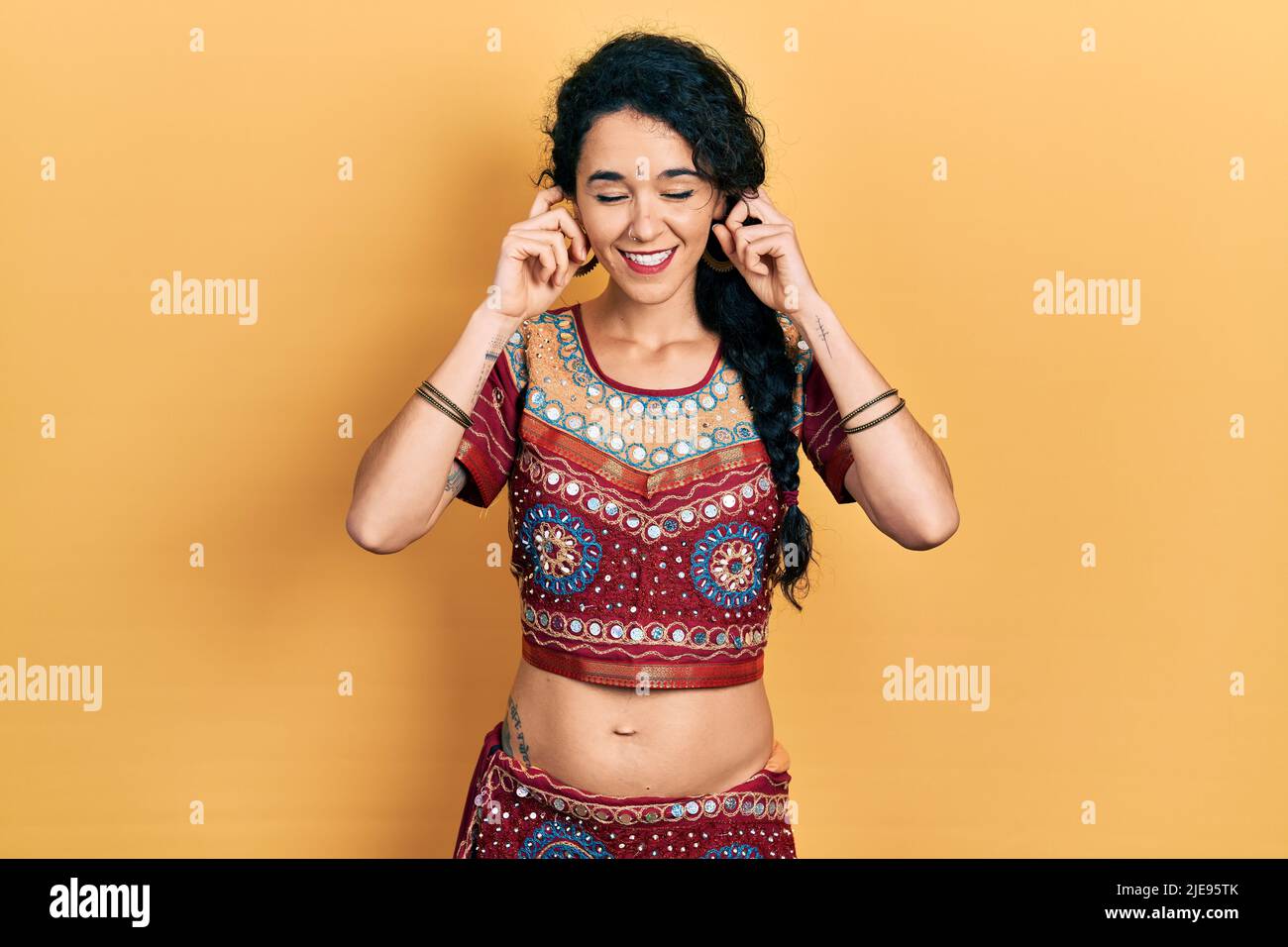 Young woman wearing bindi and bollywood clothing covering ears with fingers with annoyed ...