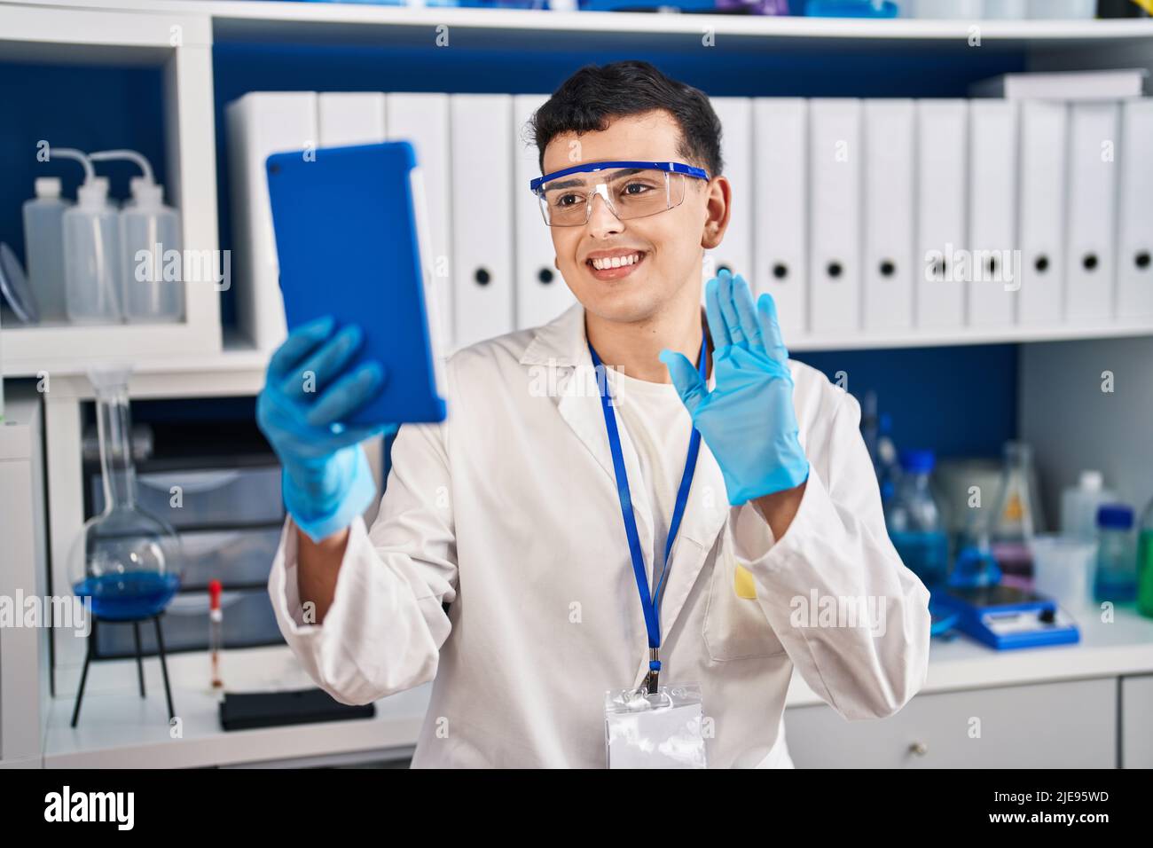 Non binary person working at scientist laboratory using tablet looking positive and happy ...
